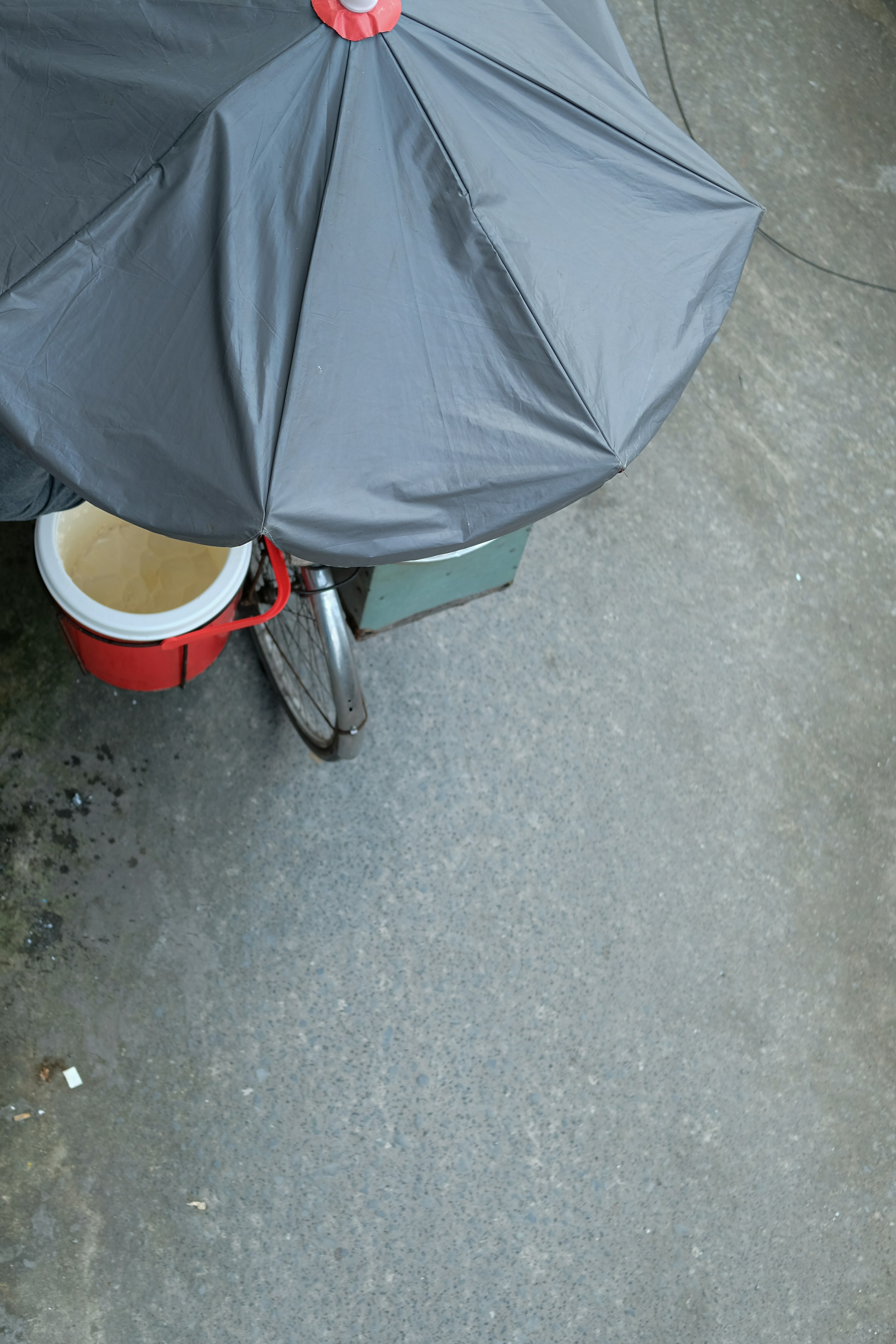 Top-Down Shield: Gray Umbrella Over a Red-Bucket Bicycle