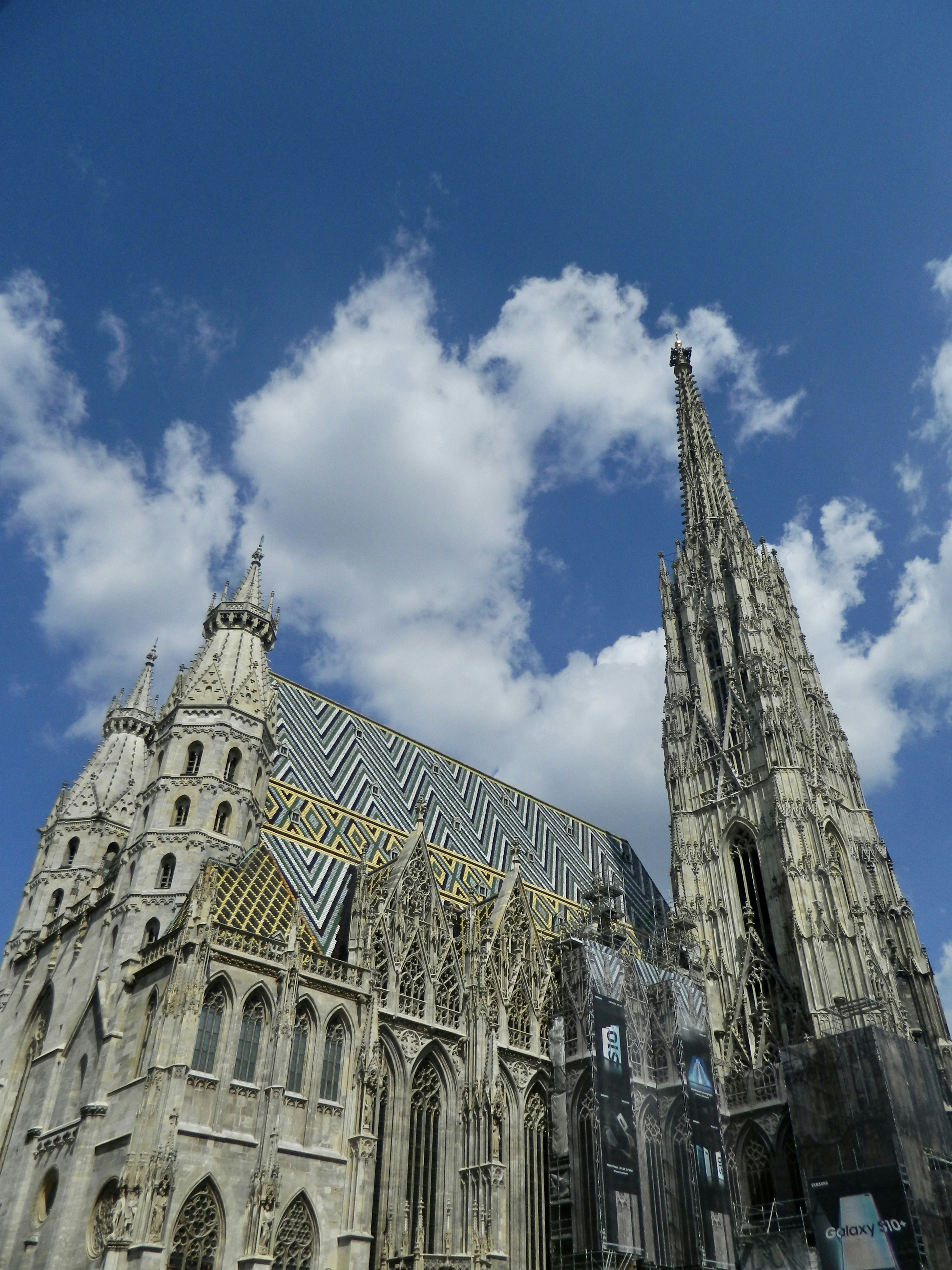 Intricate Gothic architecture of a cathedral featuring a striking patterned roof against a vibrant sky.