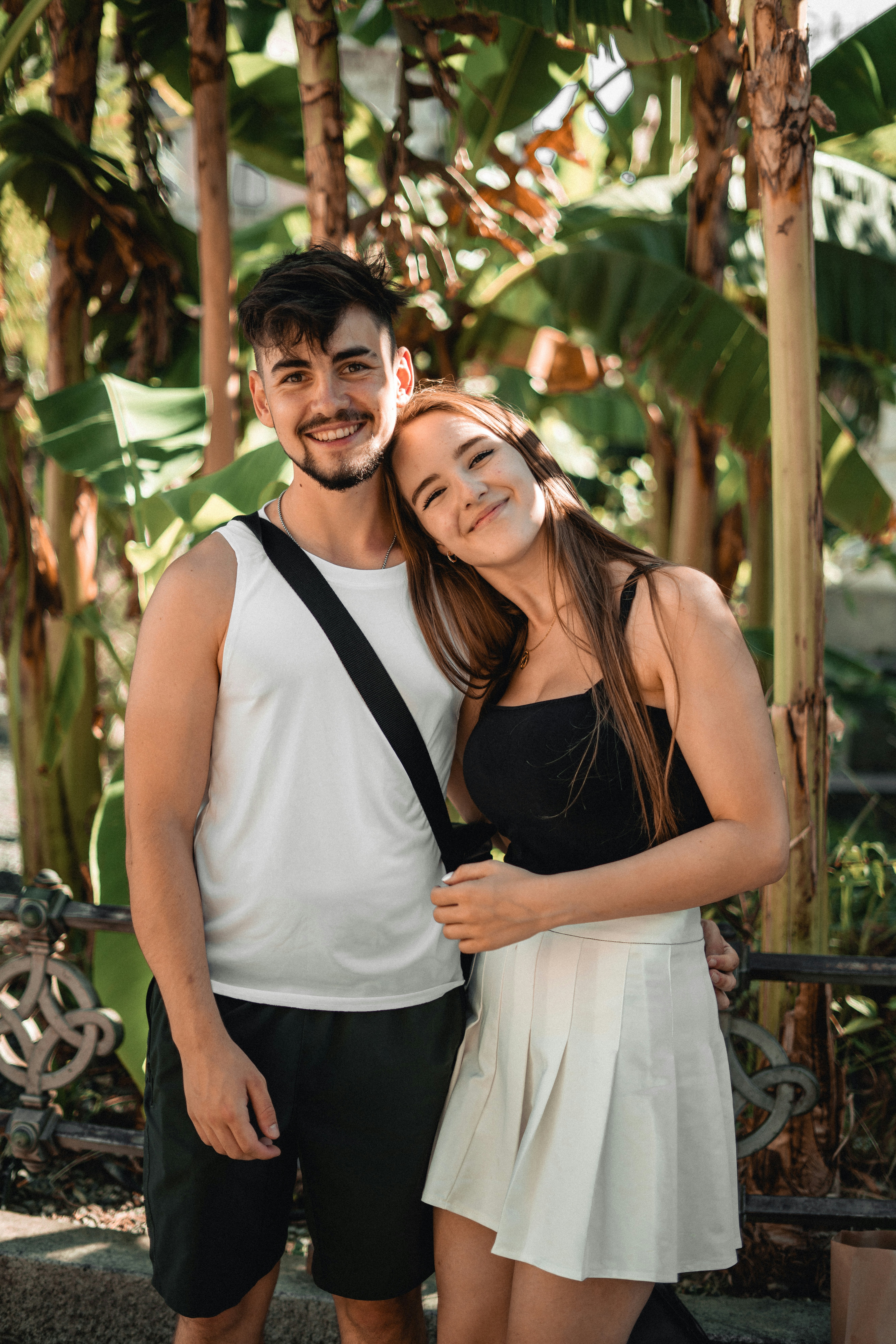 A young couple poses warmly together in a tropical setting, surrounded by vibrant banana plants.