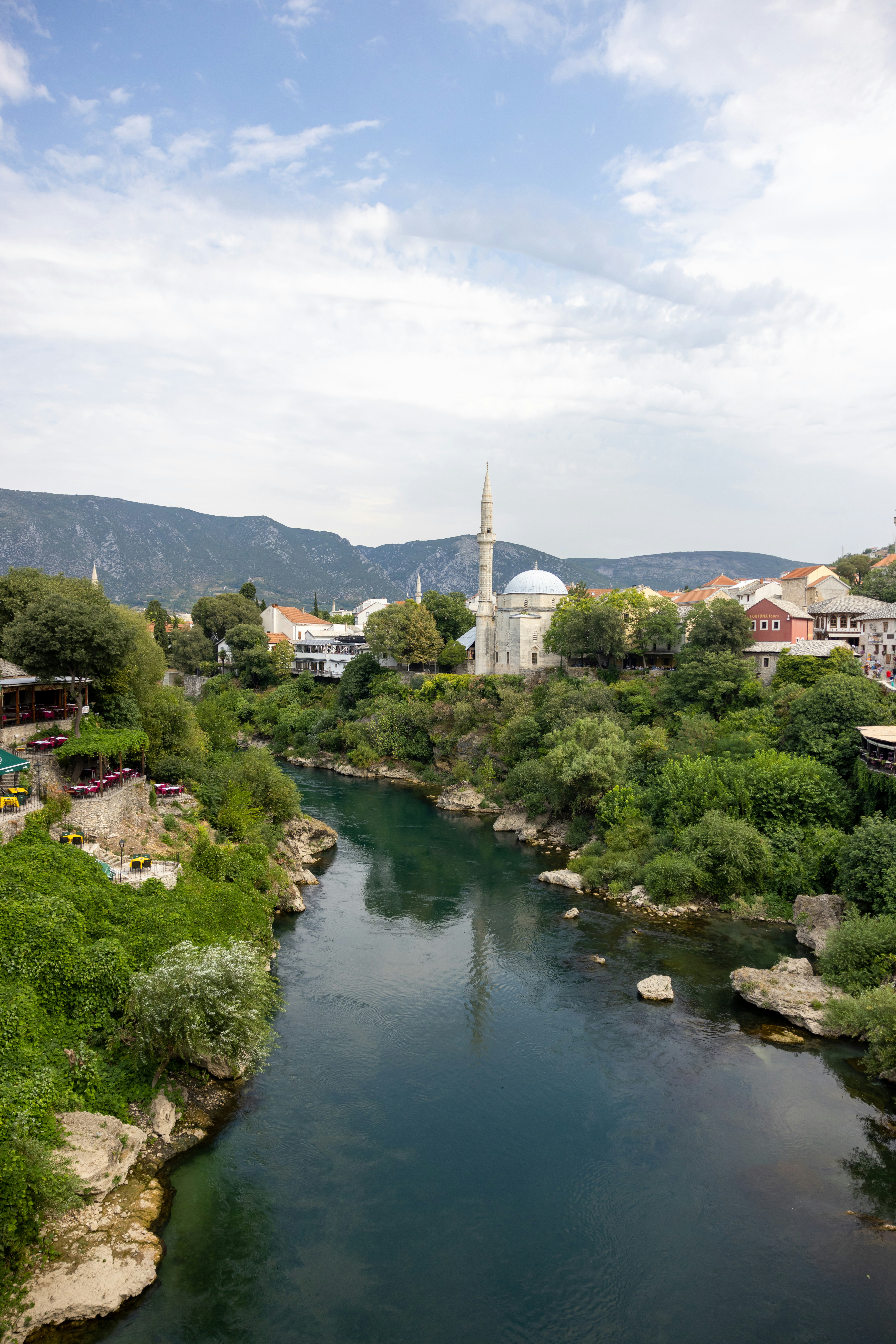 A serene river flows through a lush landscape, framed by historical architecture and vibrant greenery. The scene captures a harmonious blend of nature and culture.