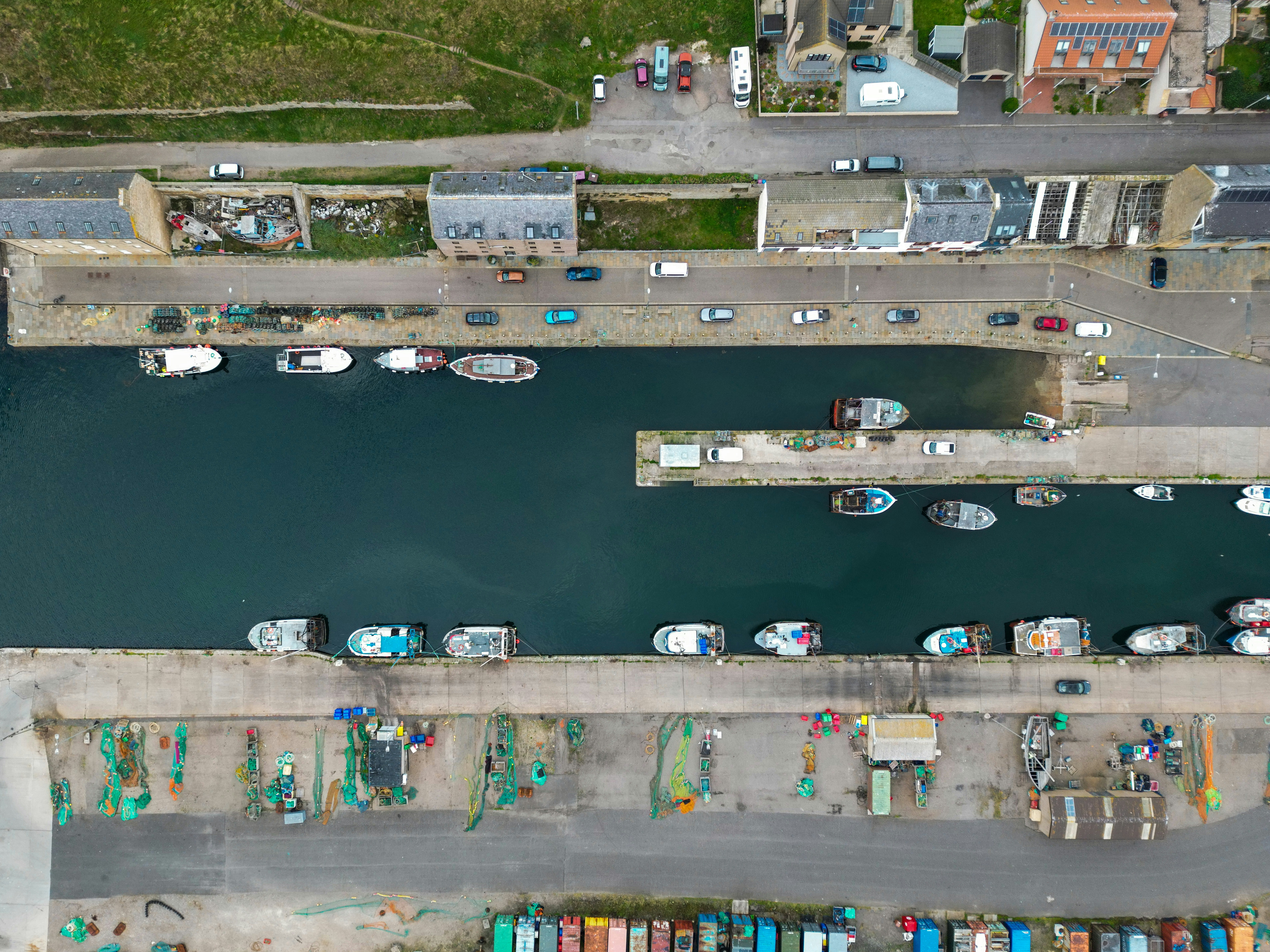 Aerial view of a port with boats docked along piers and colorful containers arranged onshore.