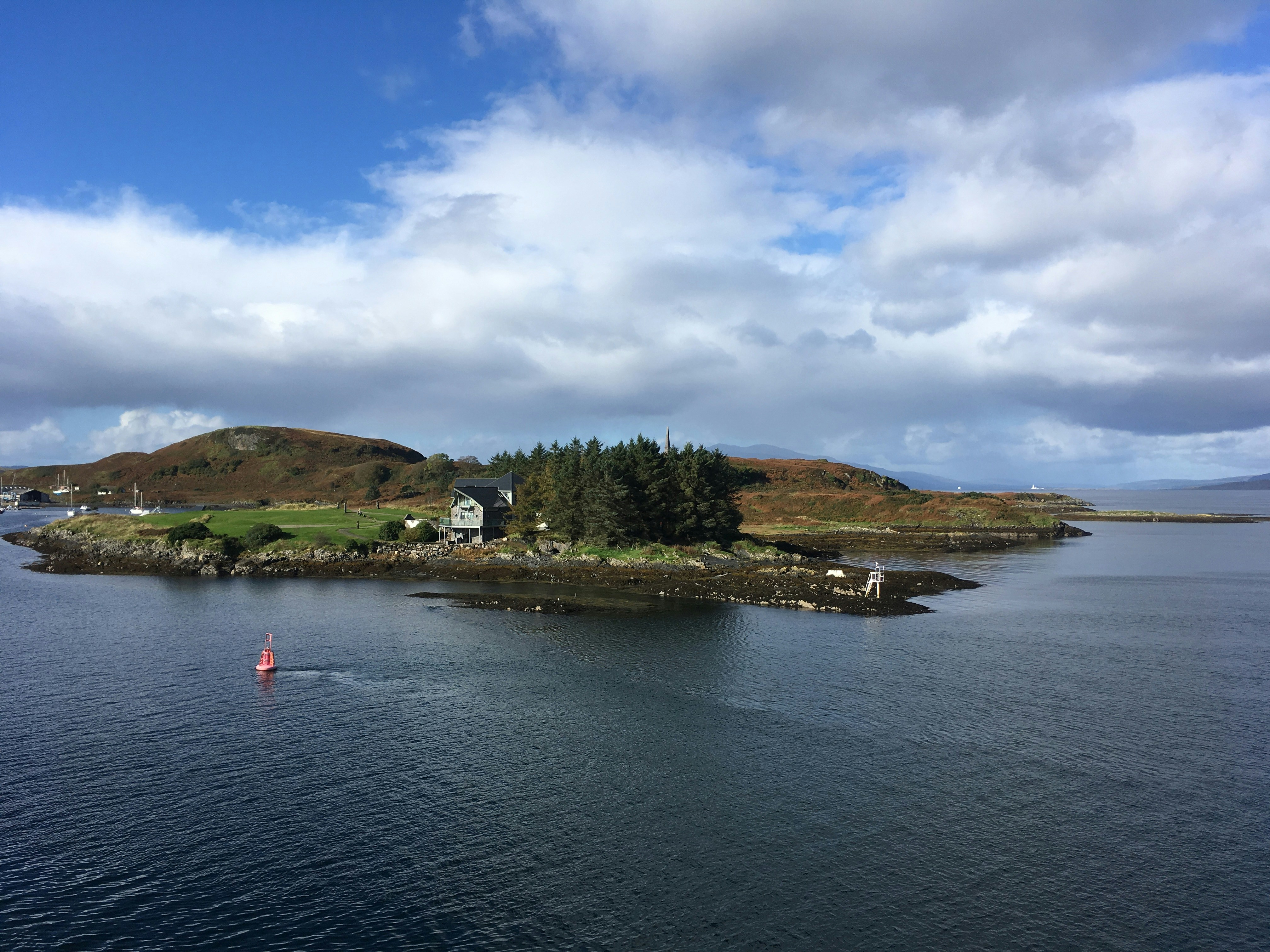 A tranquil island scene featuring a quaint house and lush greenery surrounded by calm waters and a buoy. The sky is partly cloudy, enhancing the serene atmosphere.