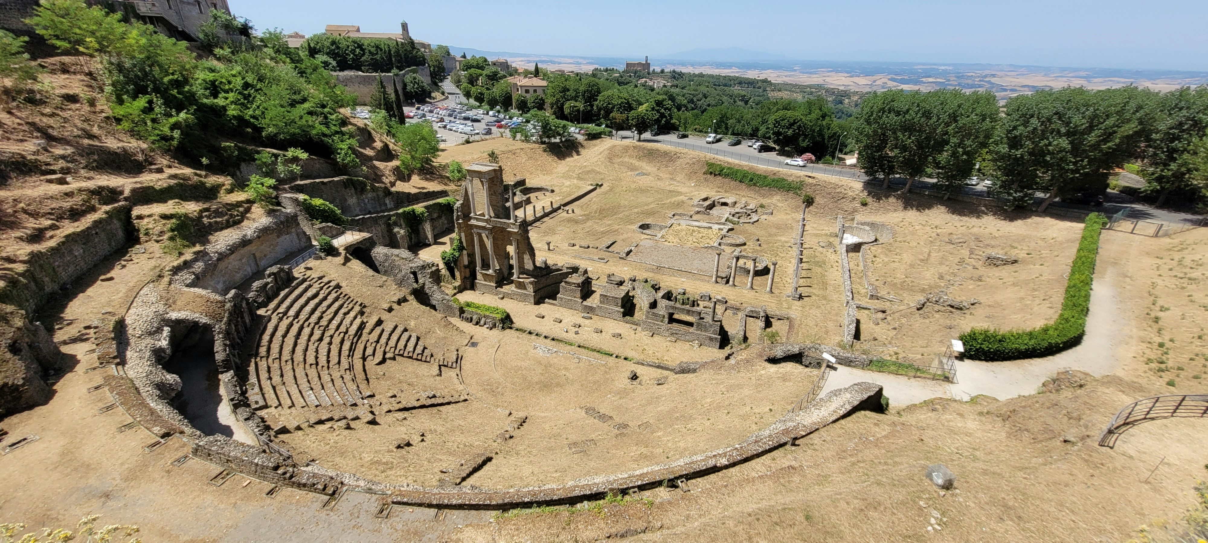 Ruins of a Roman theater nestled in a sunlit landscape, showcasing the remnants of architectural grandeur amidst dry terrain.