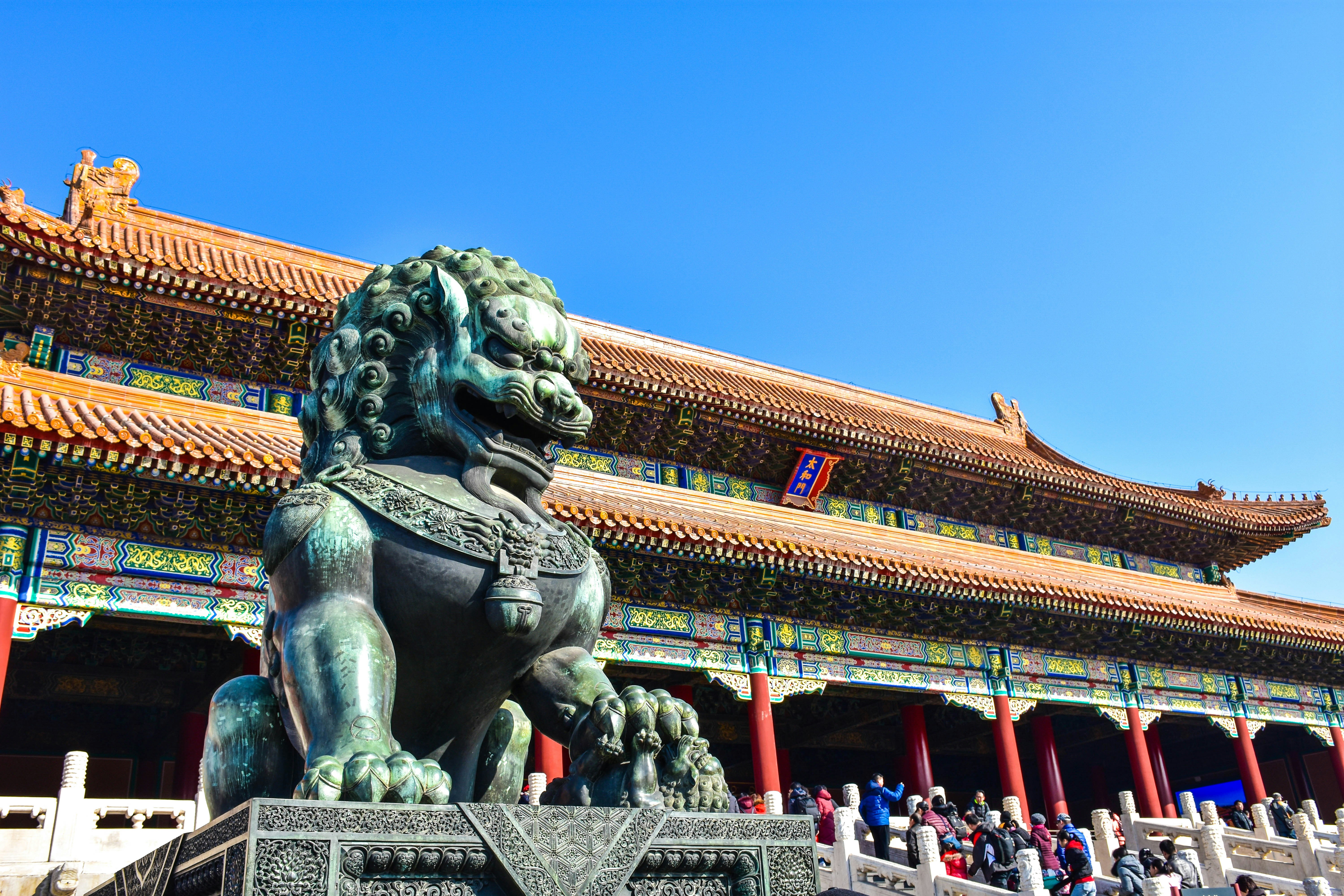 Bronze Guardian Lion Framed by a Painted Imperial Courtyard Under a Cerulean Sky
