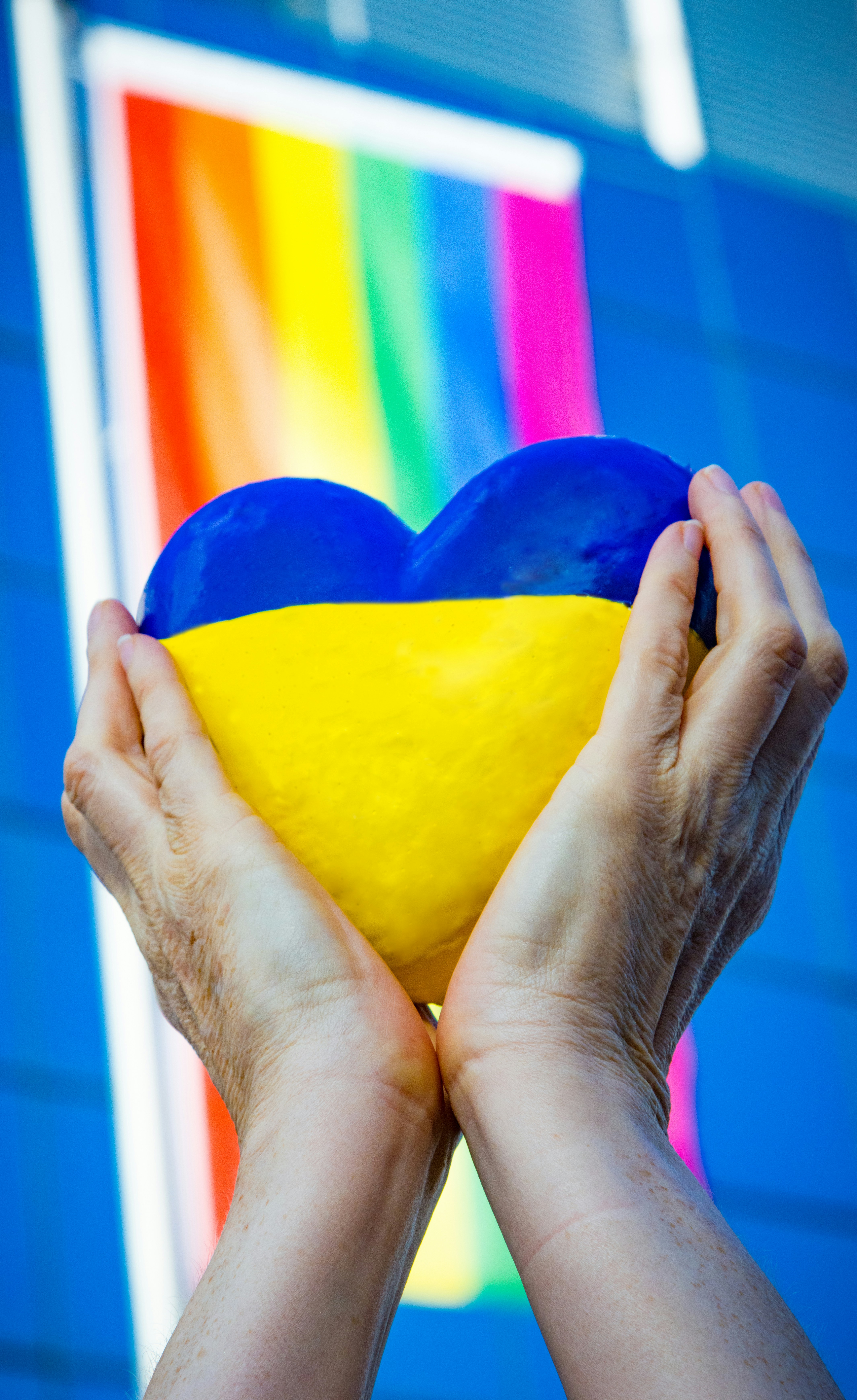 Hands Cradling a Two-Toned Heart Against a Rainbow Backdrop