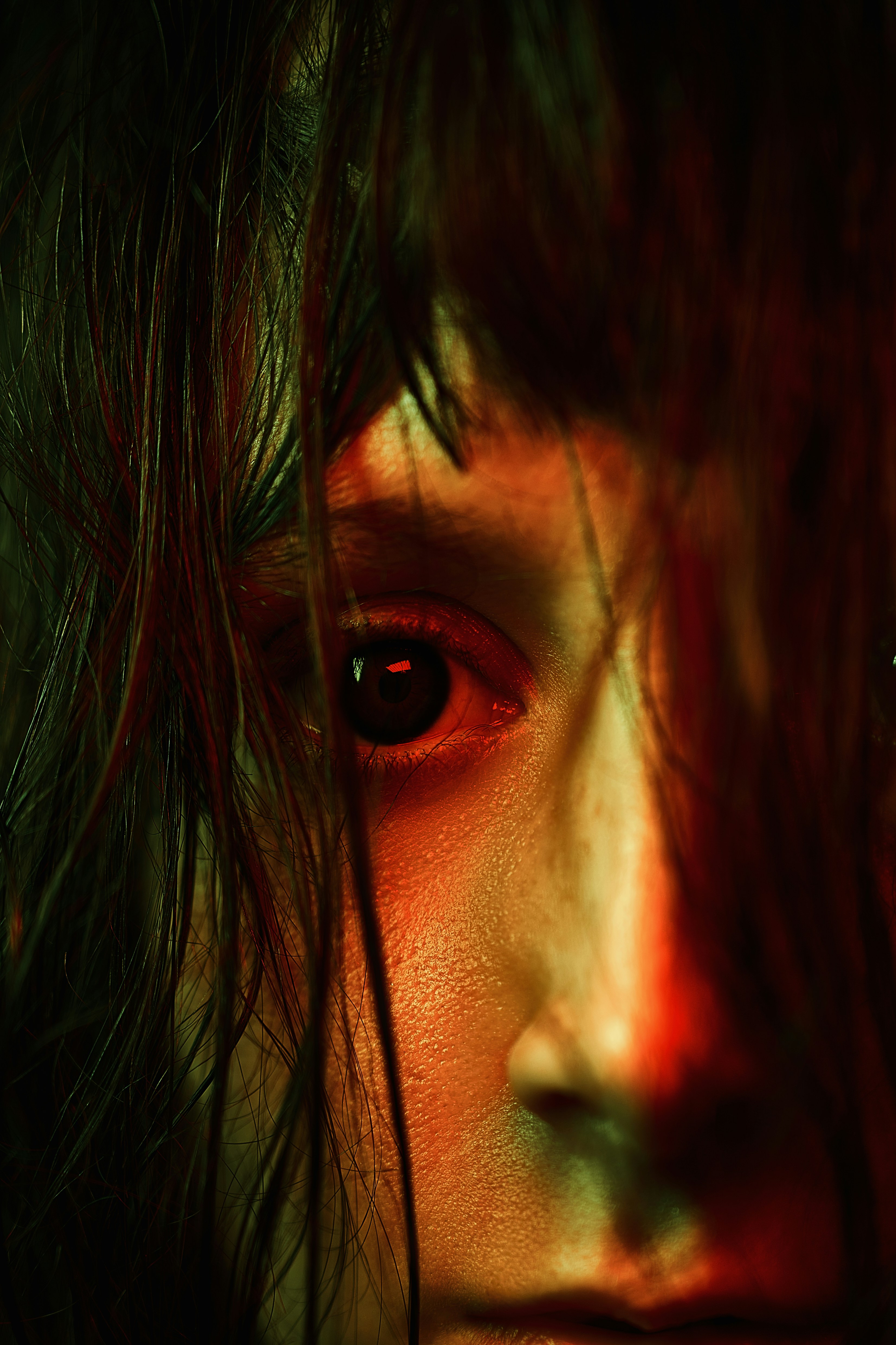 Close-up portrait emphasizing a gaze obscured by wet hair, illuminated with dramatic red and green lighting. The expression conveys a sense of mystery.