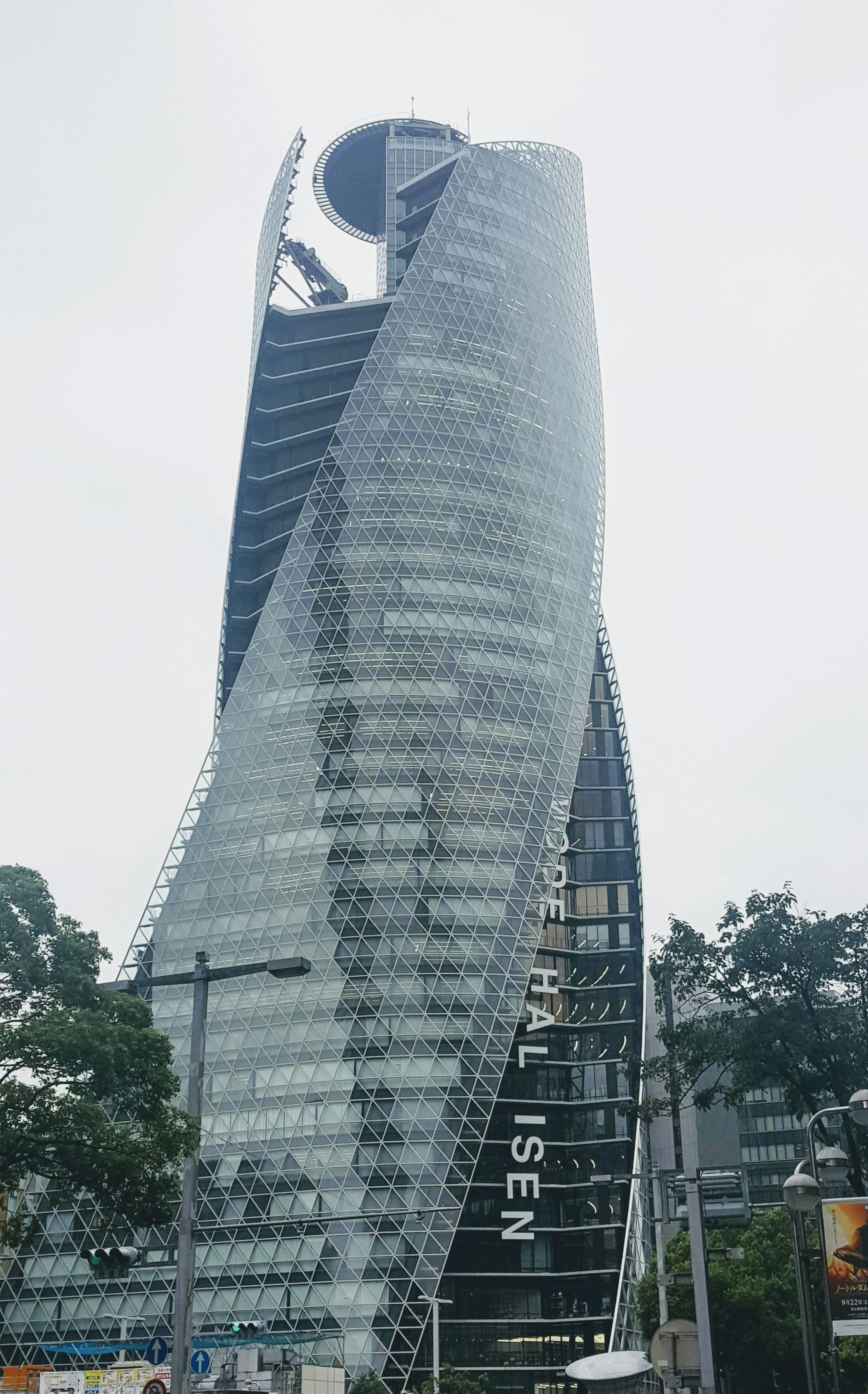 A twisted glass skyscraper with a latticed facade rises above the street. A circular opening at the top adds a futuristic focal point.