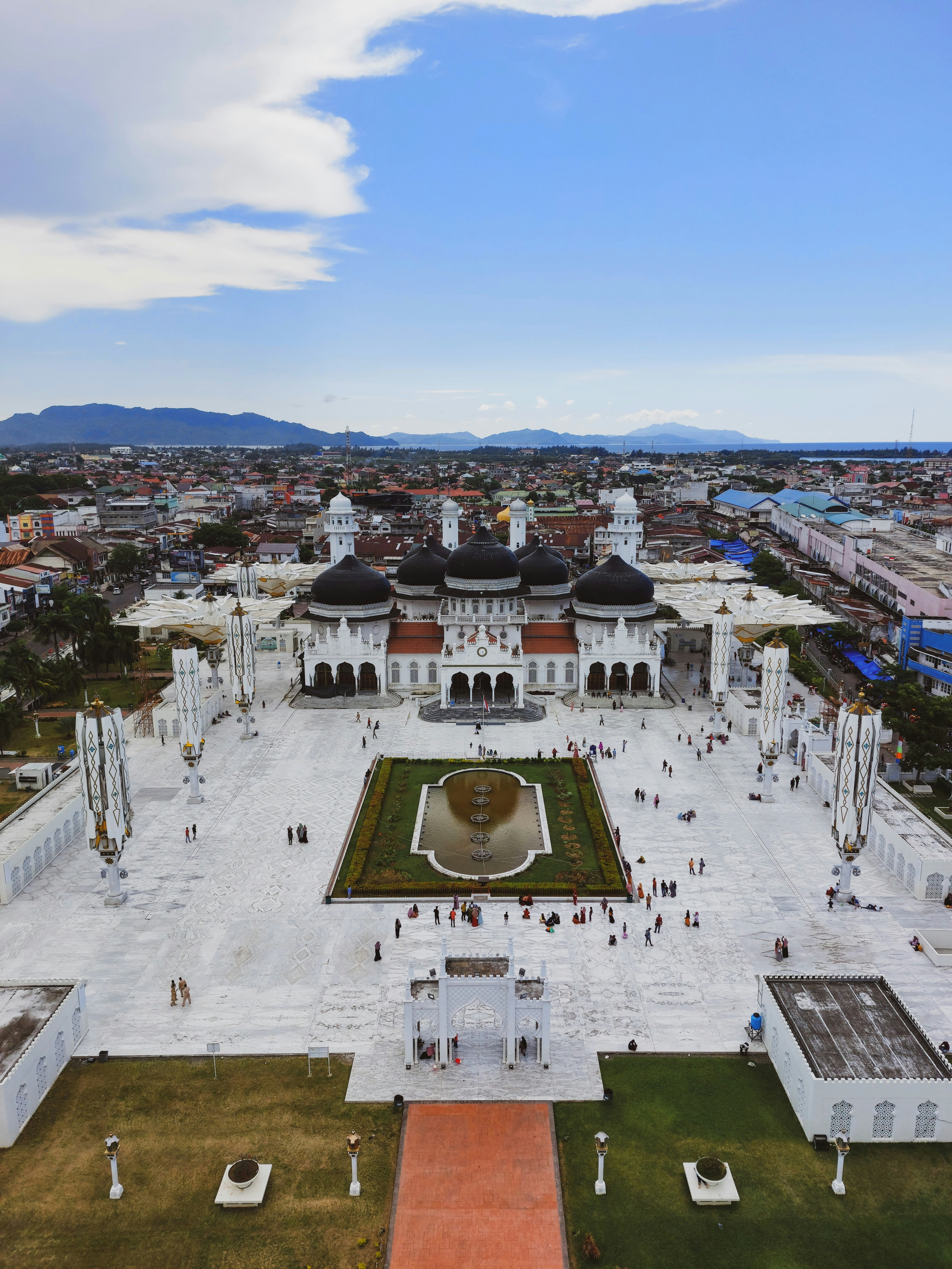 Aerial view of a grand mosque surrounded by vibrant city life, showcasing intricate architecture and a central fountain. The scene captures the harmony between urban and spiritual spaces.