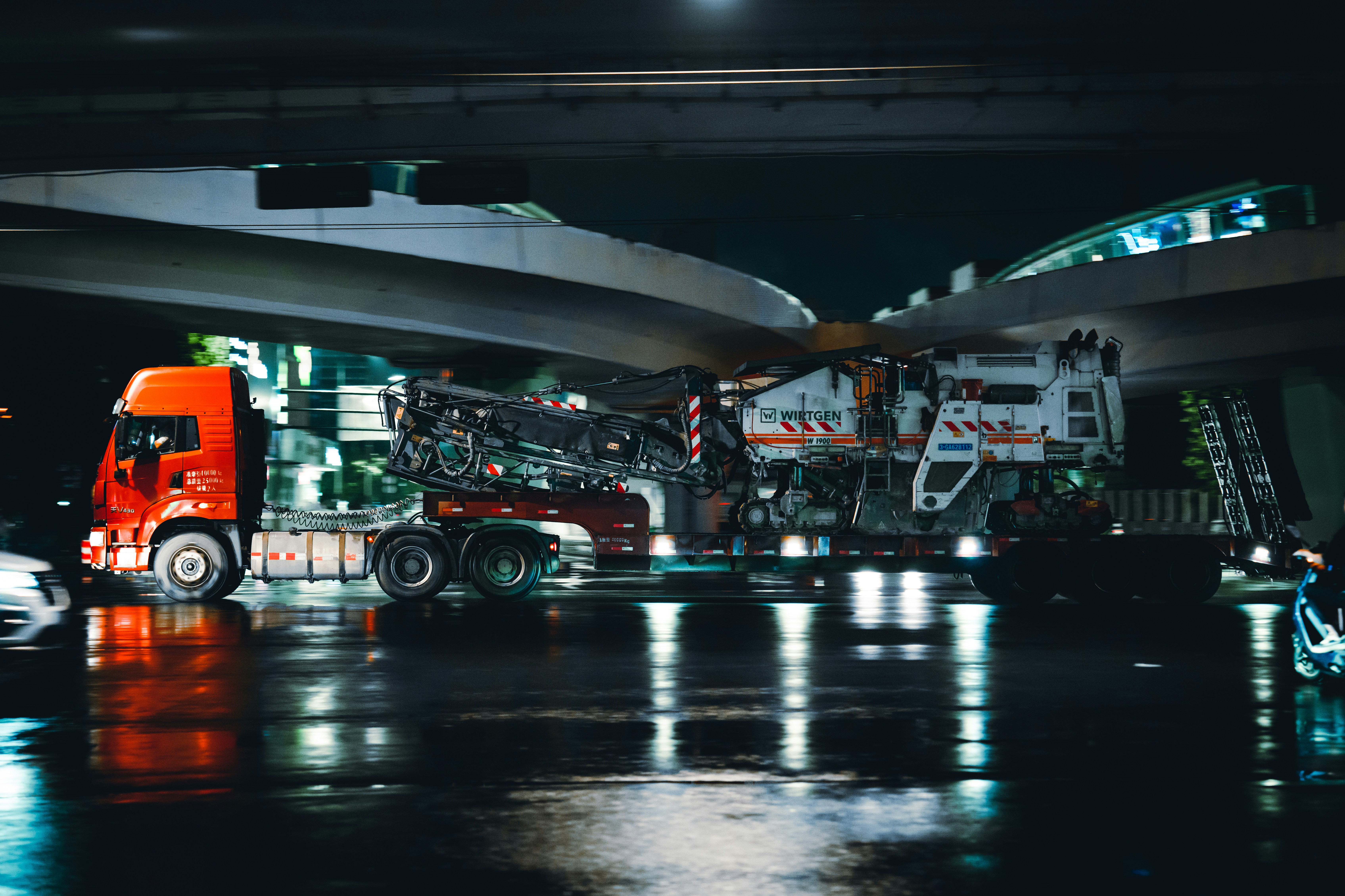 Nocturnal Lift Under the Overpass: Red Truck with a Crane Trailer Casts Neon Reflections