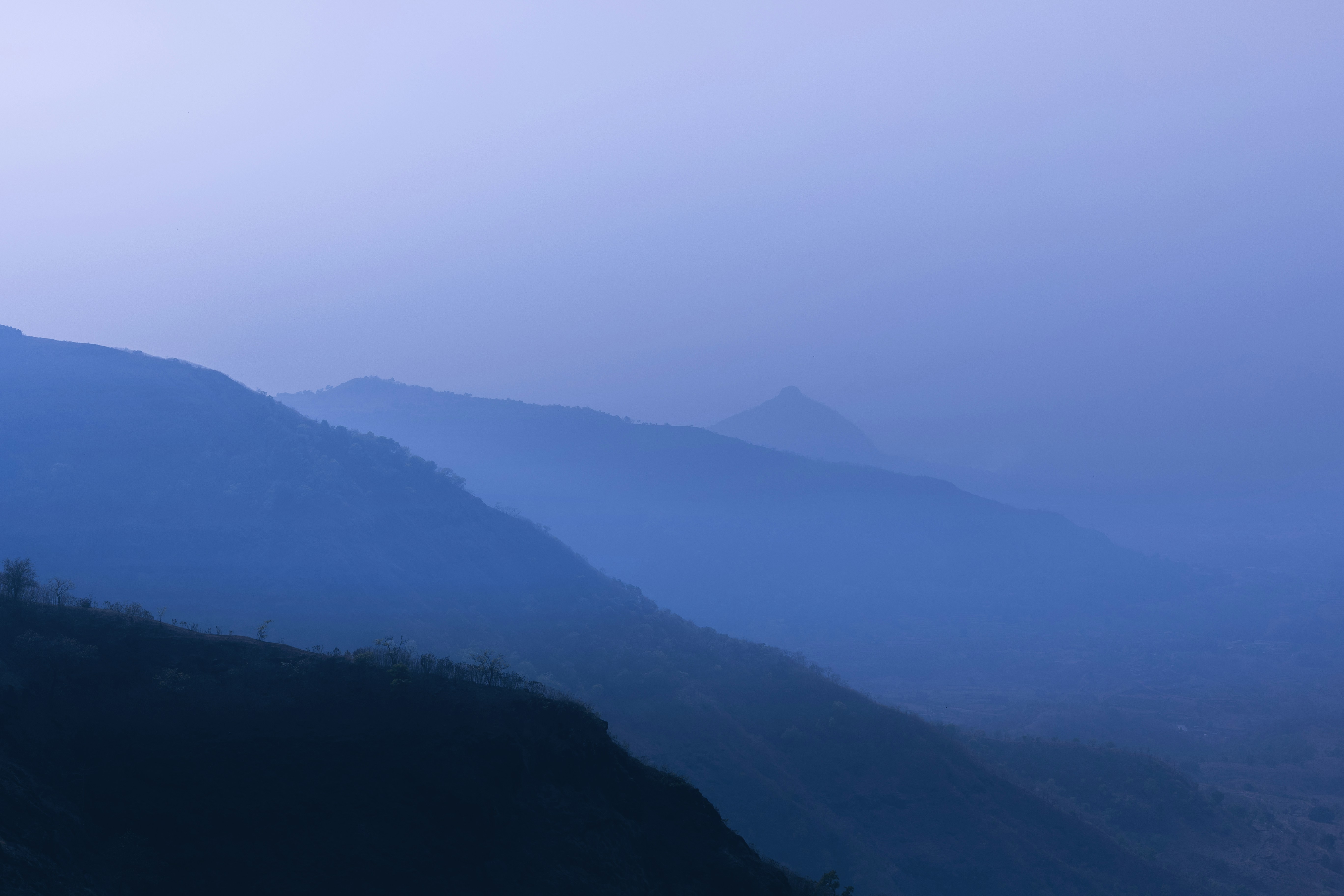 Misty mountain range enveloped in soft blue fog under a serene sky.