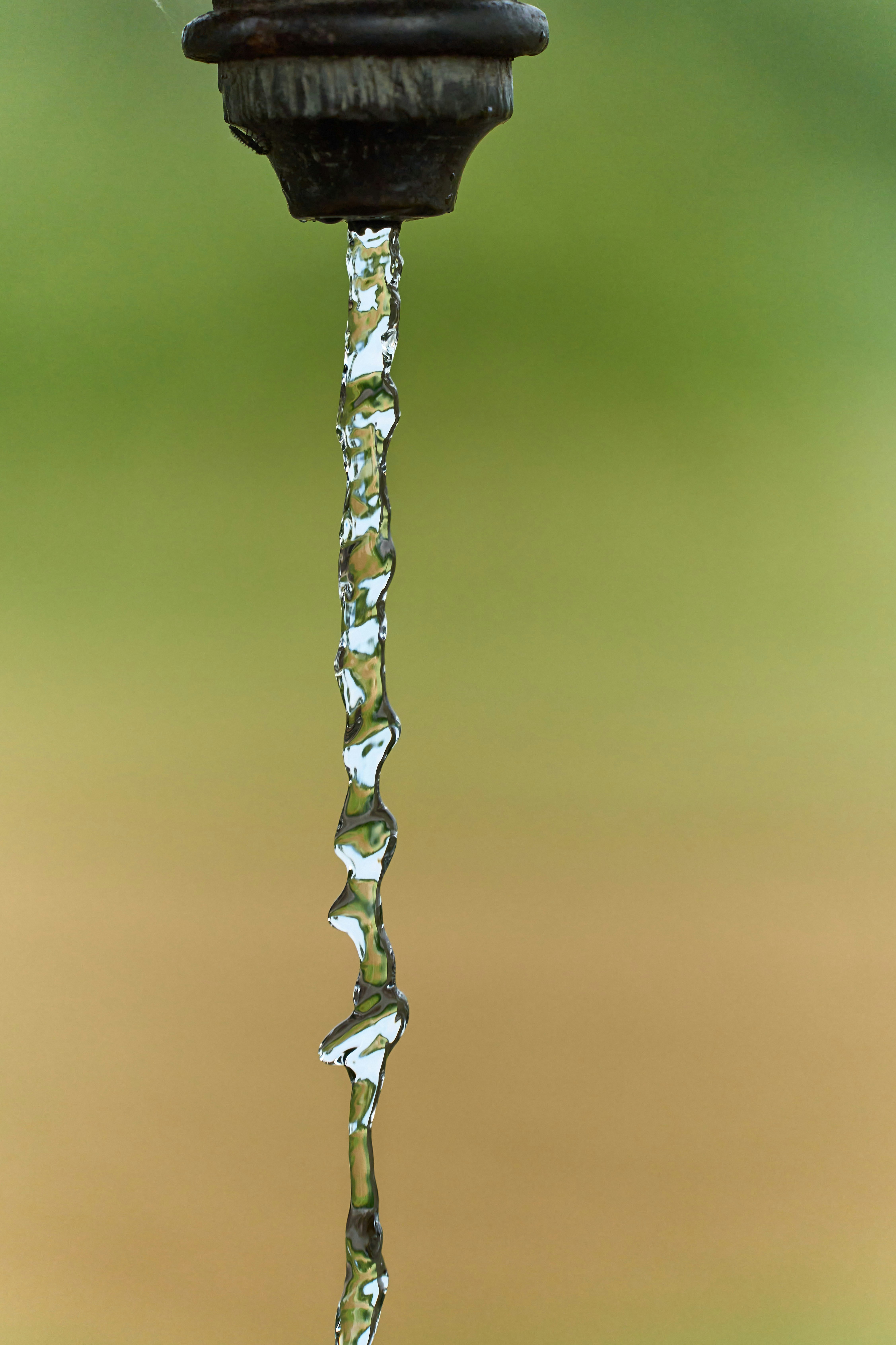 Water cascading from a faucet, captured in mid-flow against a blurred green background.