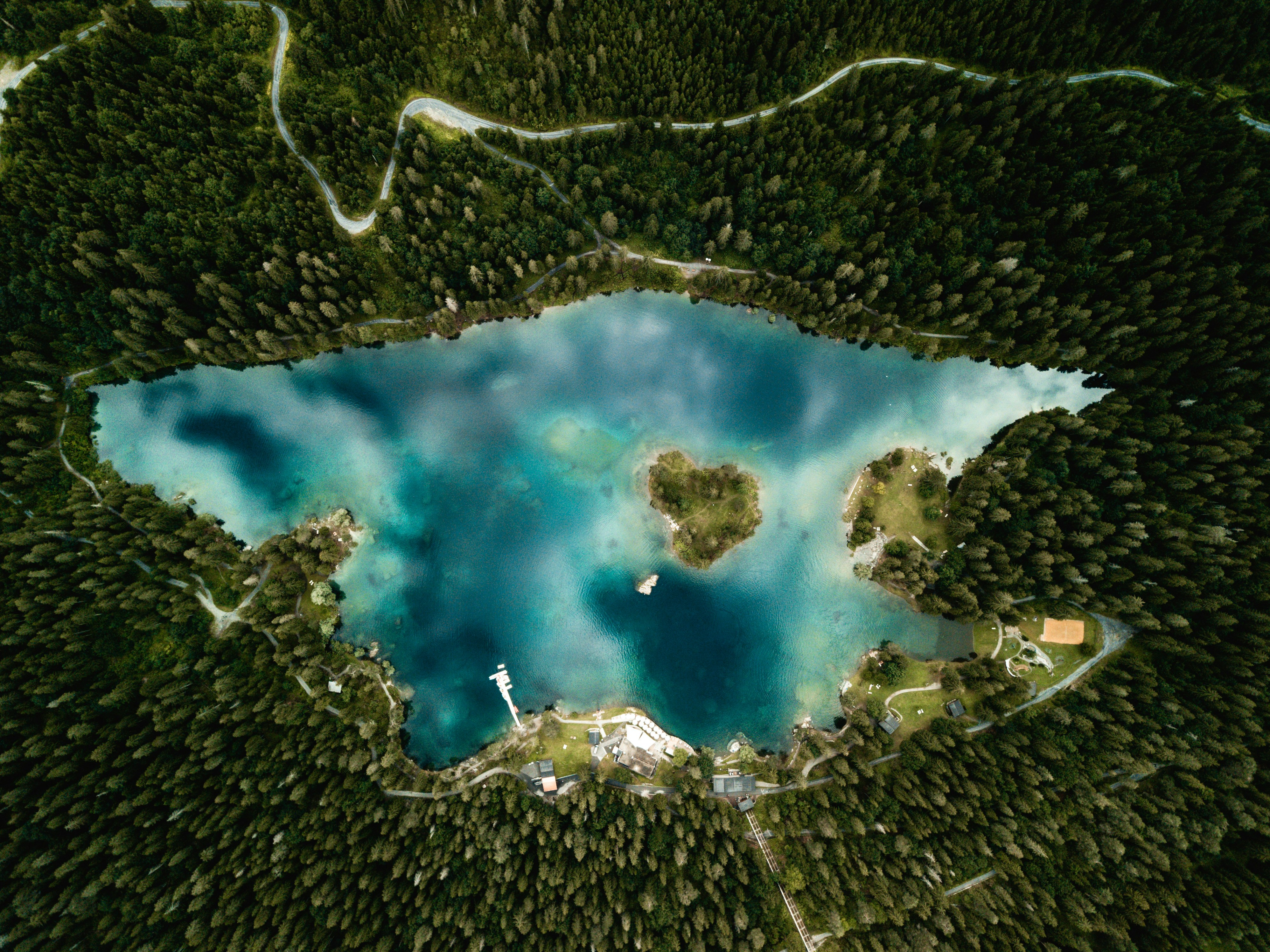 Aerial view of a heart-shaped lake surrounded by lush forests, with a hint of turquoise water reflecting the landscape. The scene captures tranquility and natural beauty.