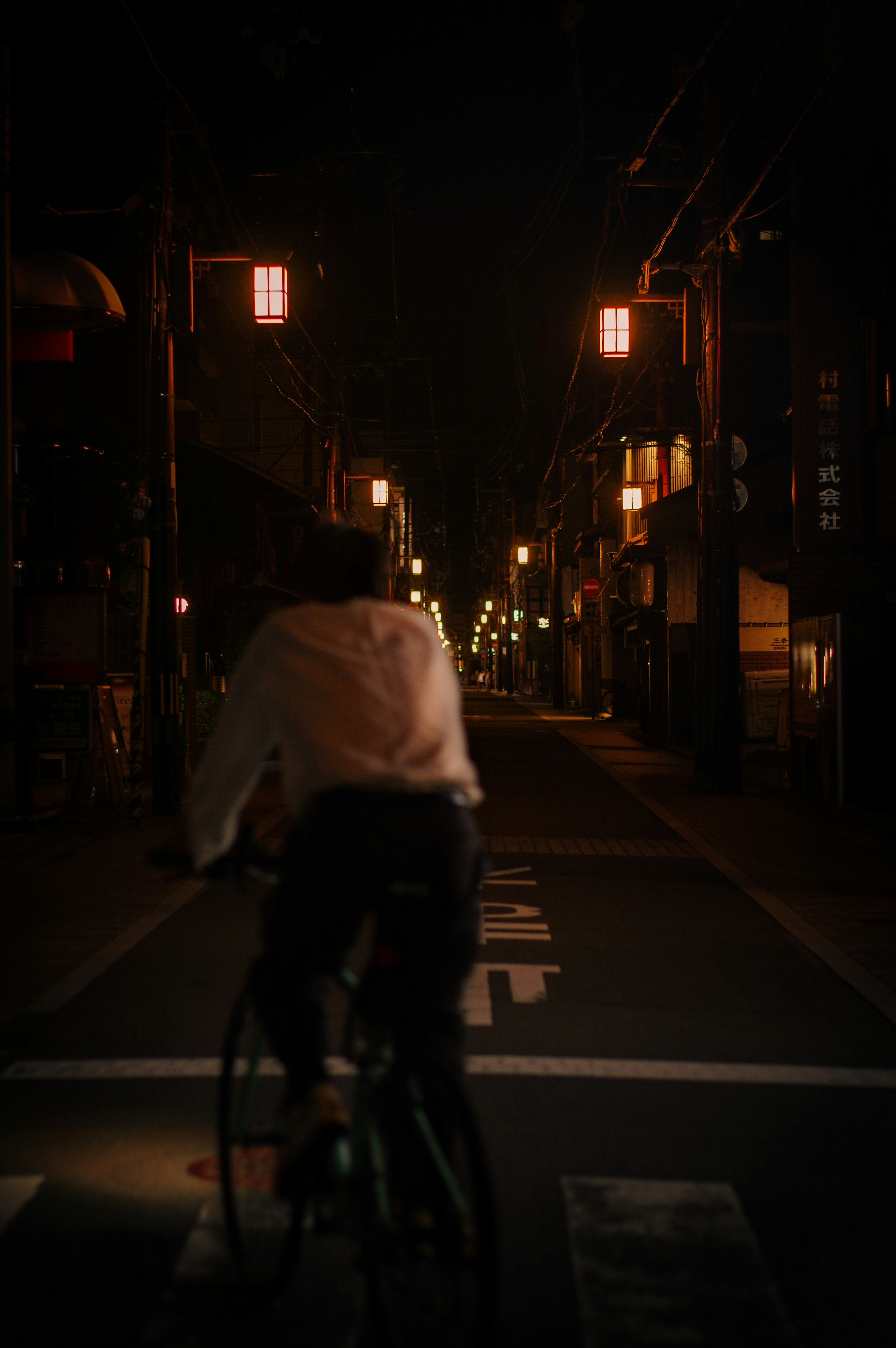 A cyclist glides through a dimly lit street adorned with glowing lanterns, evoking a sense of tranquility in the stillness of night.