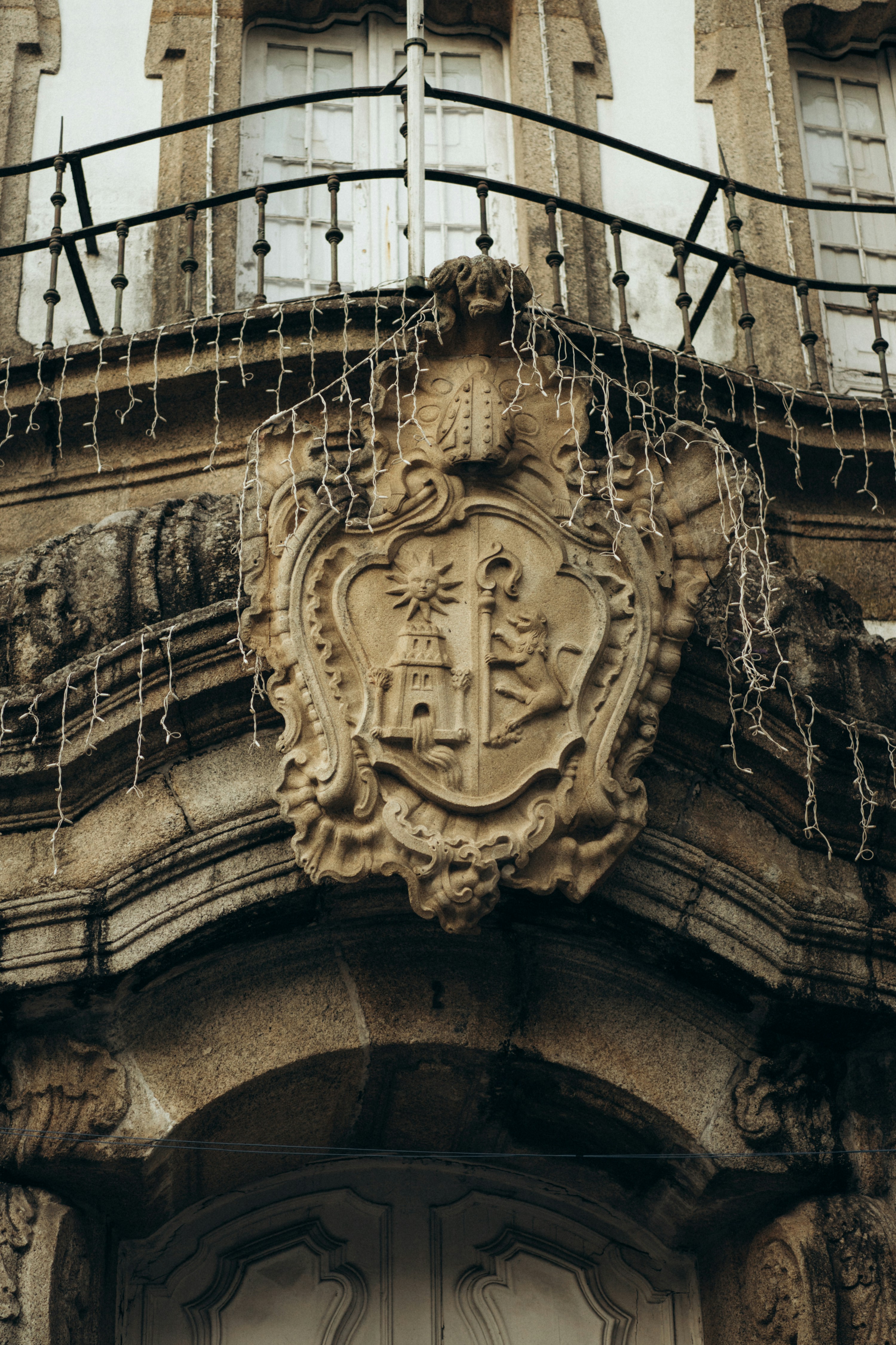 Intricate stone blazonry adorns a historic building facade beneath delicate hanging lights.