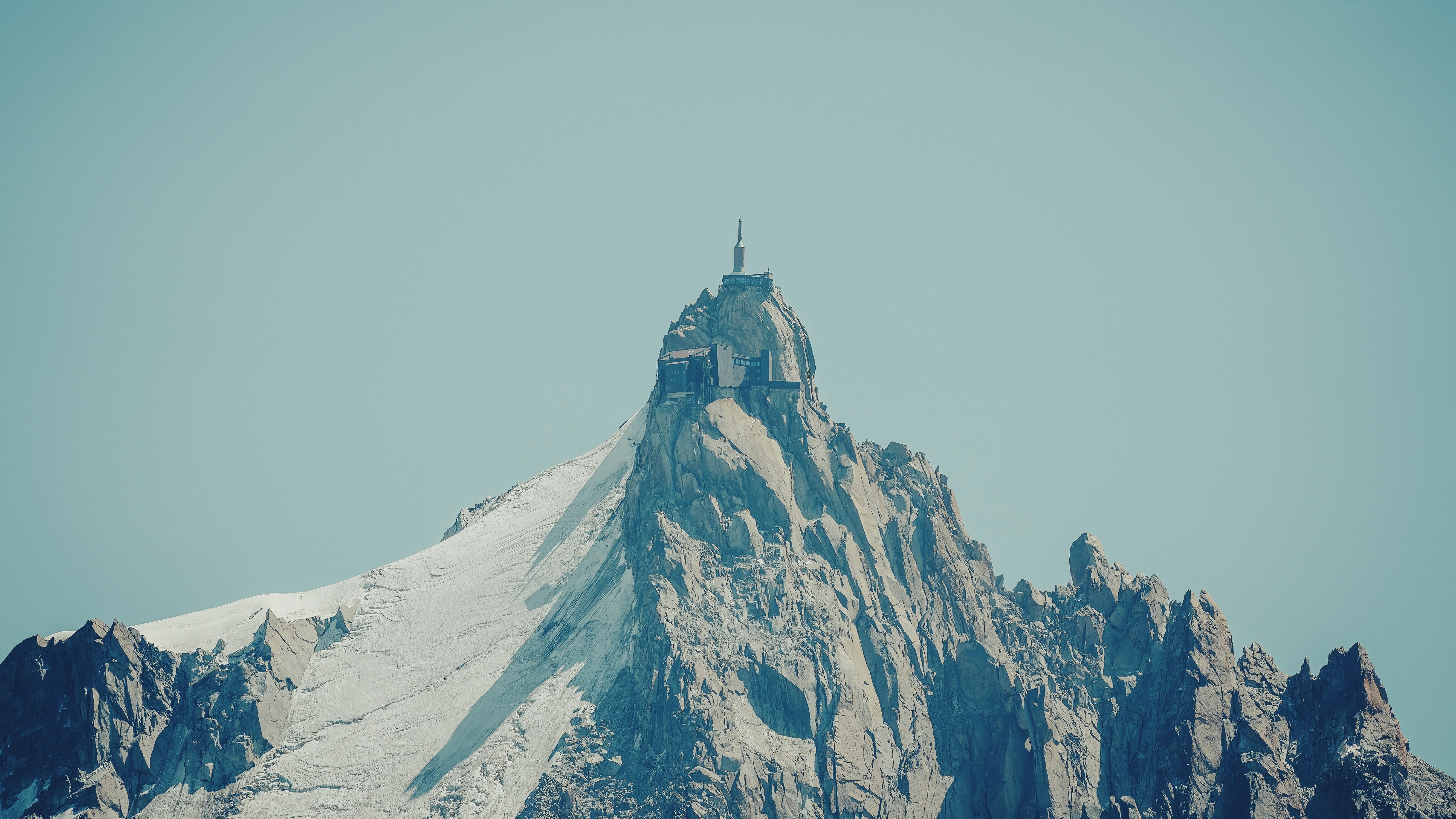 Majestic mountain peak crowned with a historic structure, surrounded by rugged terrain and a clear sky. The snow-capped summit reflects the resilience of nature.