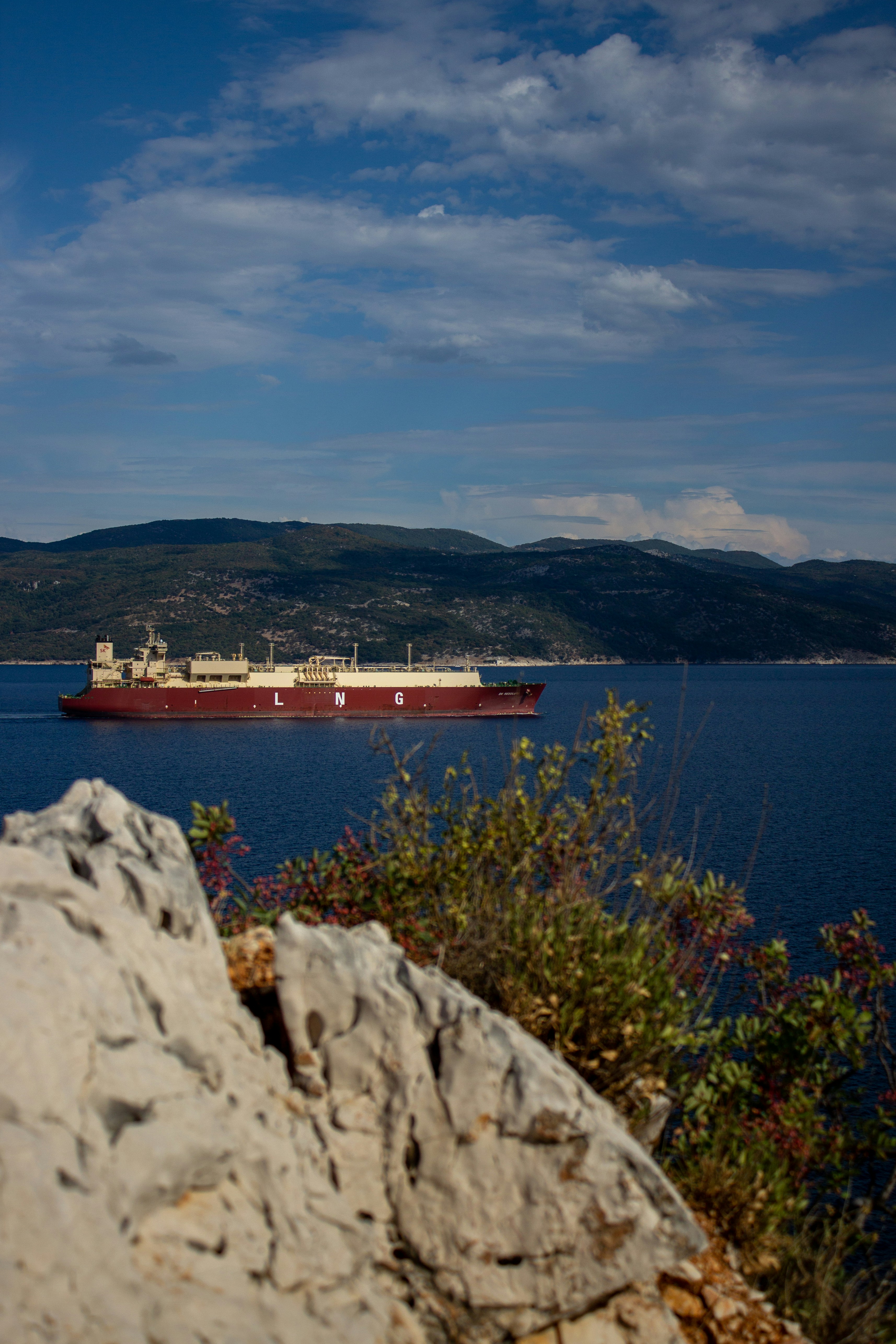 Red Cargo Vessel Against Blue Horizon, Framed by Craggy Shore