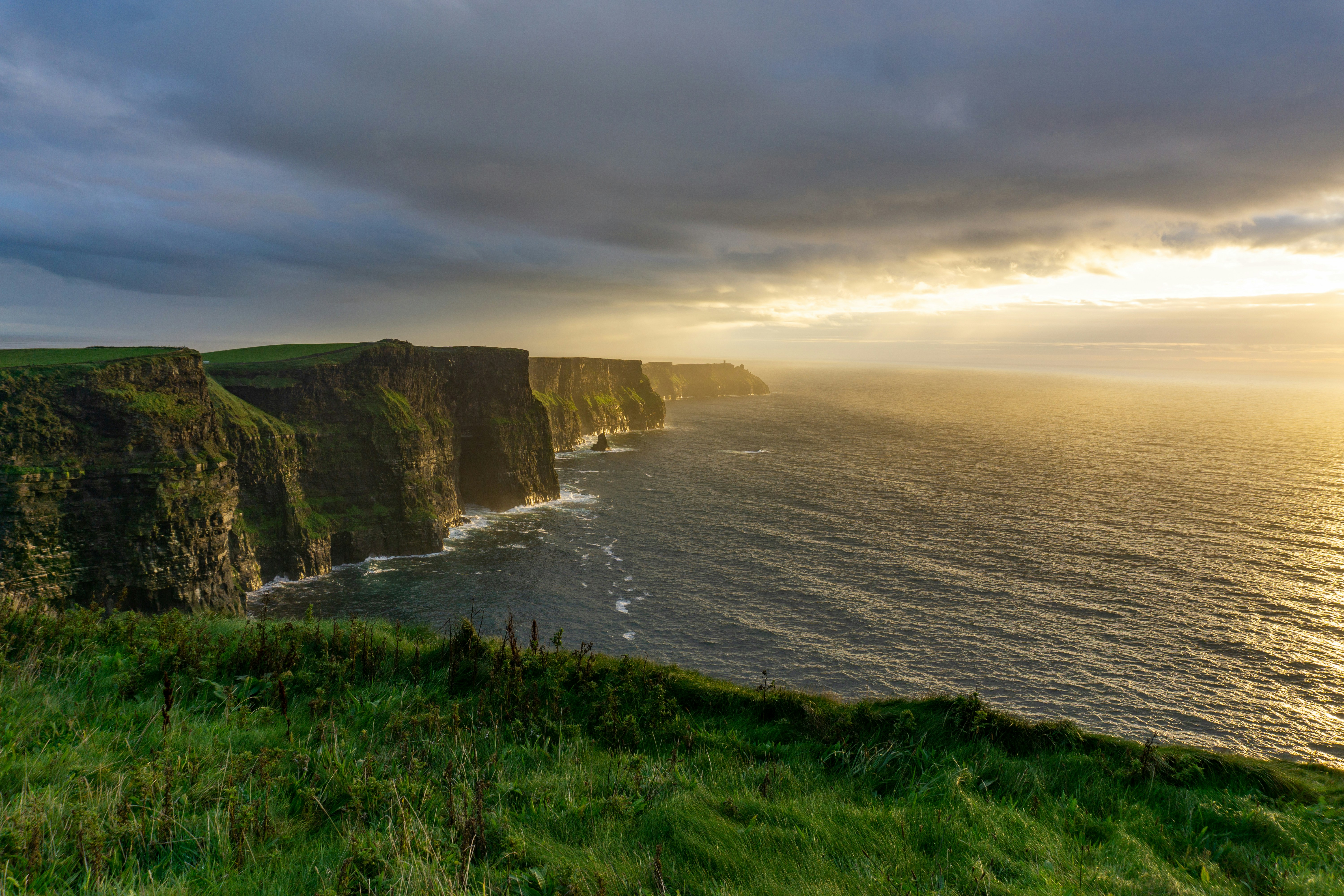 Dramatic cliffs overlooking the ocean under a golden sunset sky.