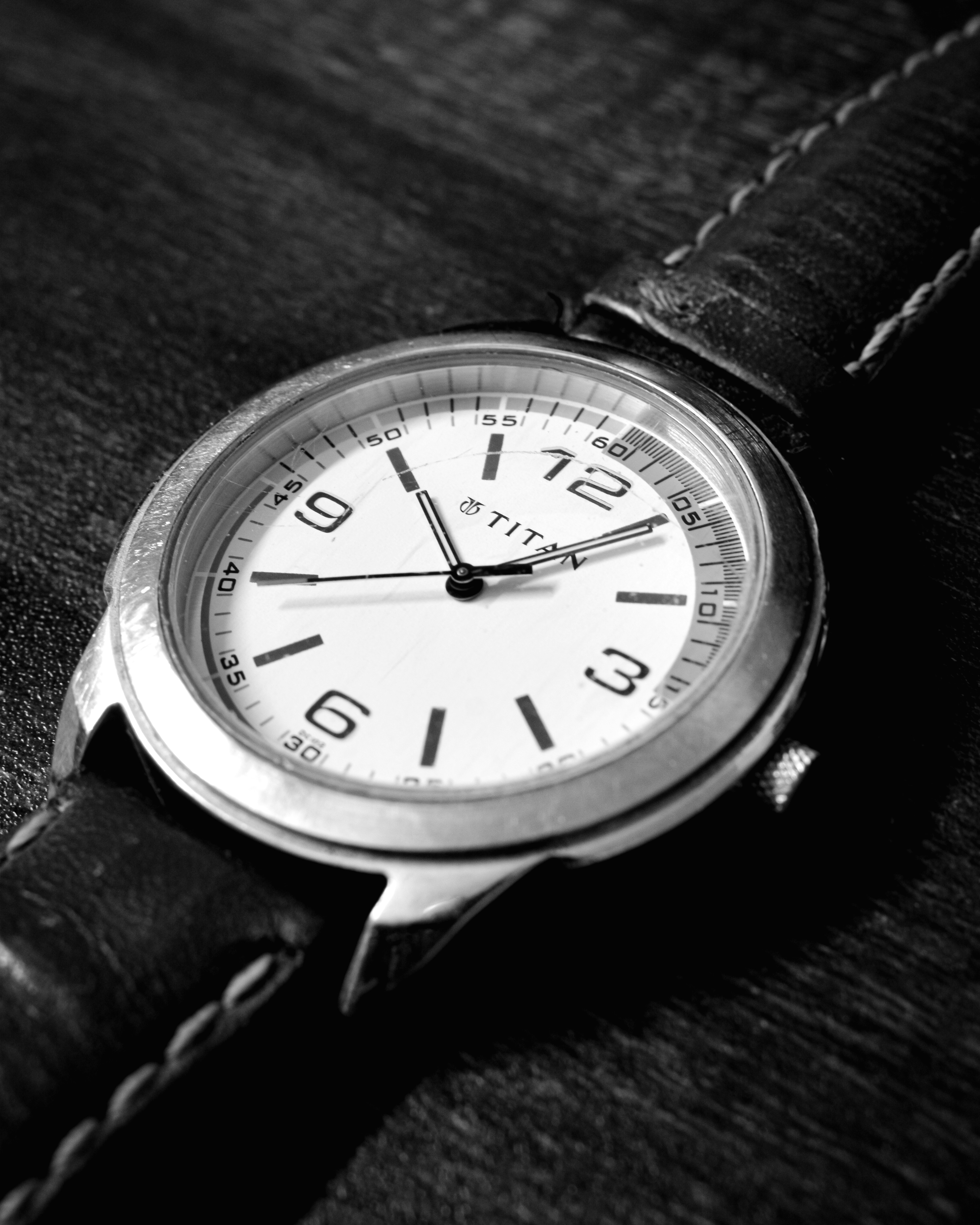Close-up of a minimalist wristwatch with a white dial and black leather strap, showcasing its classic design and craftsmanship.