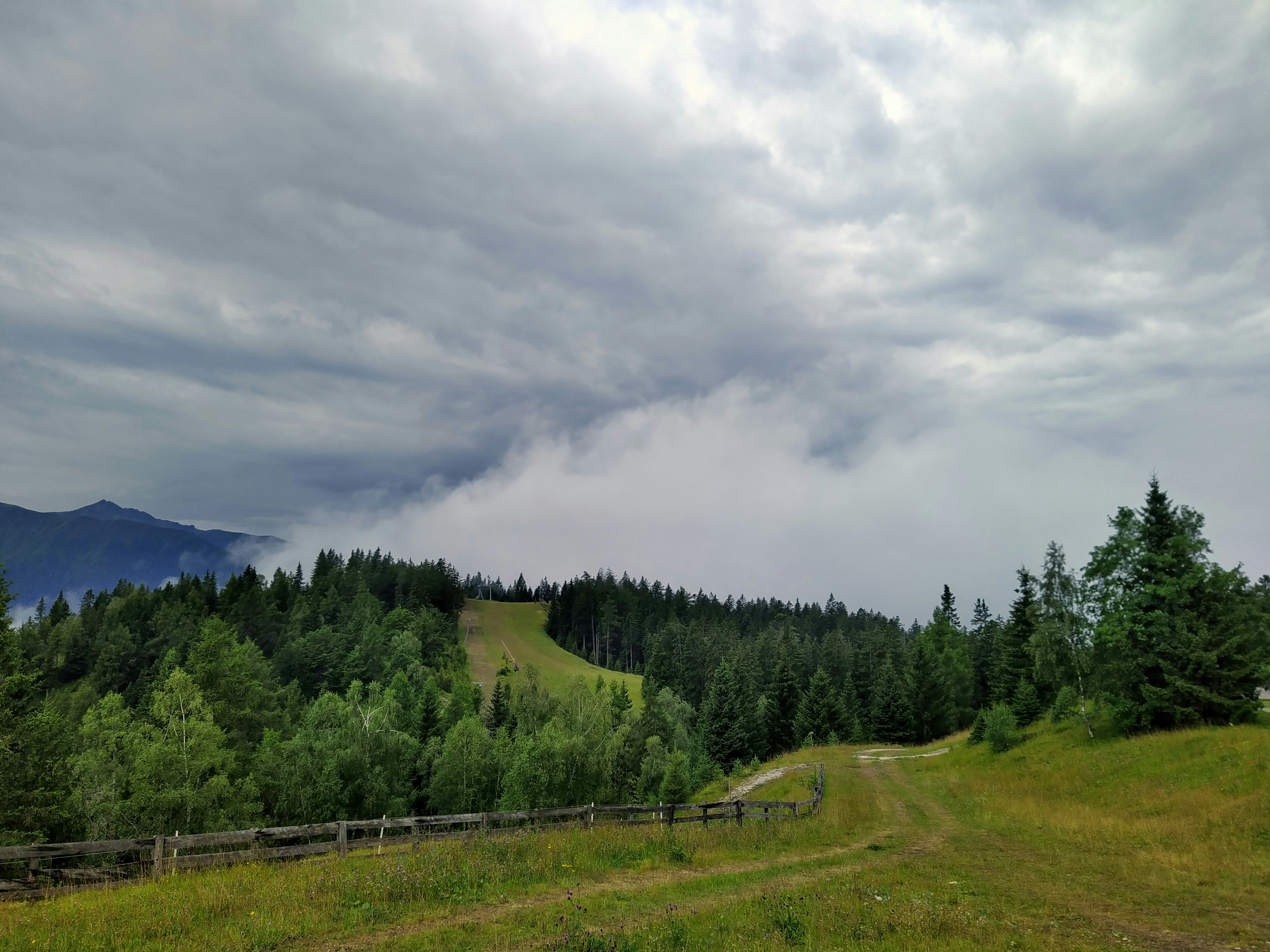 Landscape photograph of a grassy hillside, a winding path, and a wooden fence beneath a cloud-filled sky.