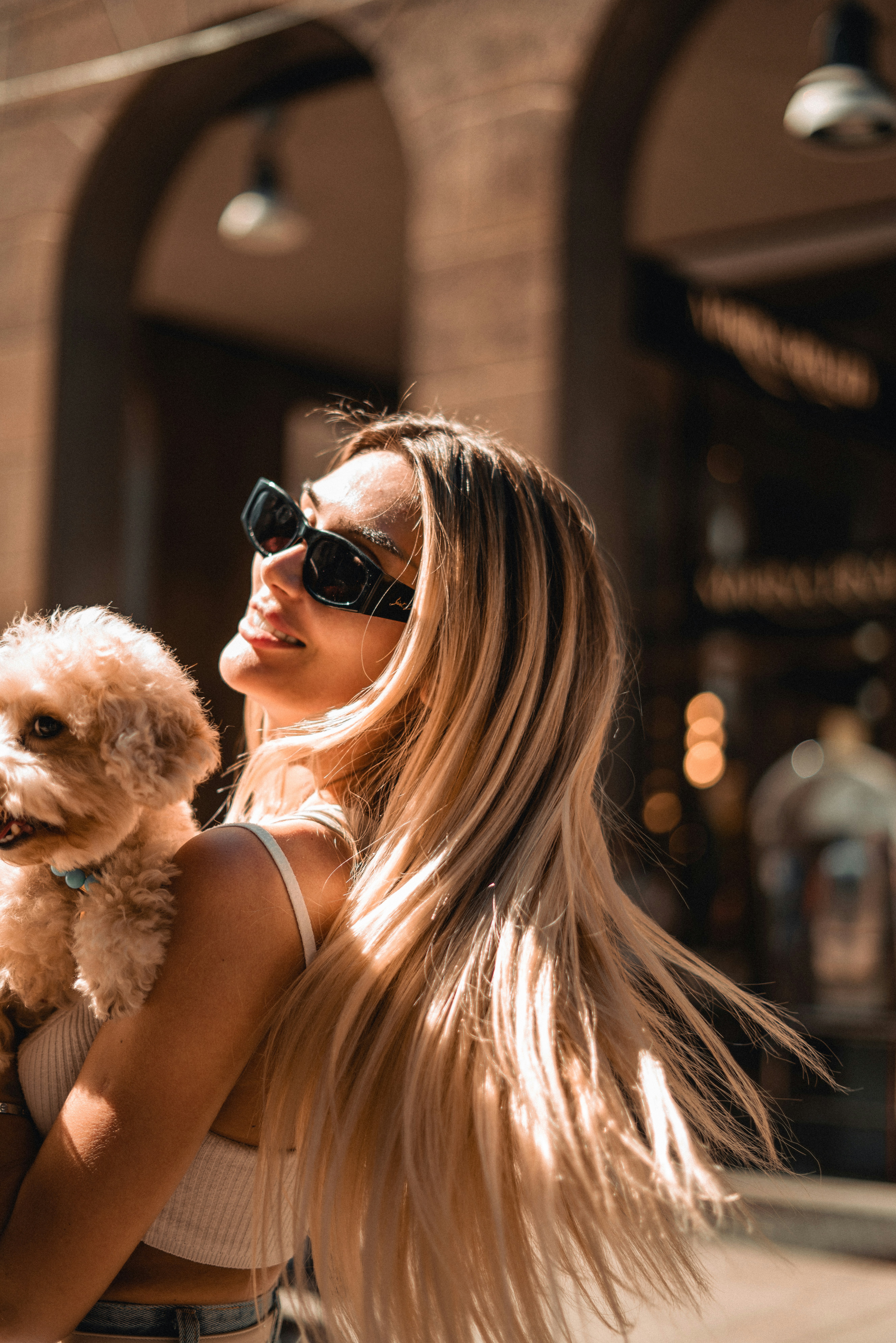 Sunlit Arcades Duo: Blonde in Sunglasses with a Fluffy Companion