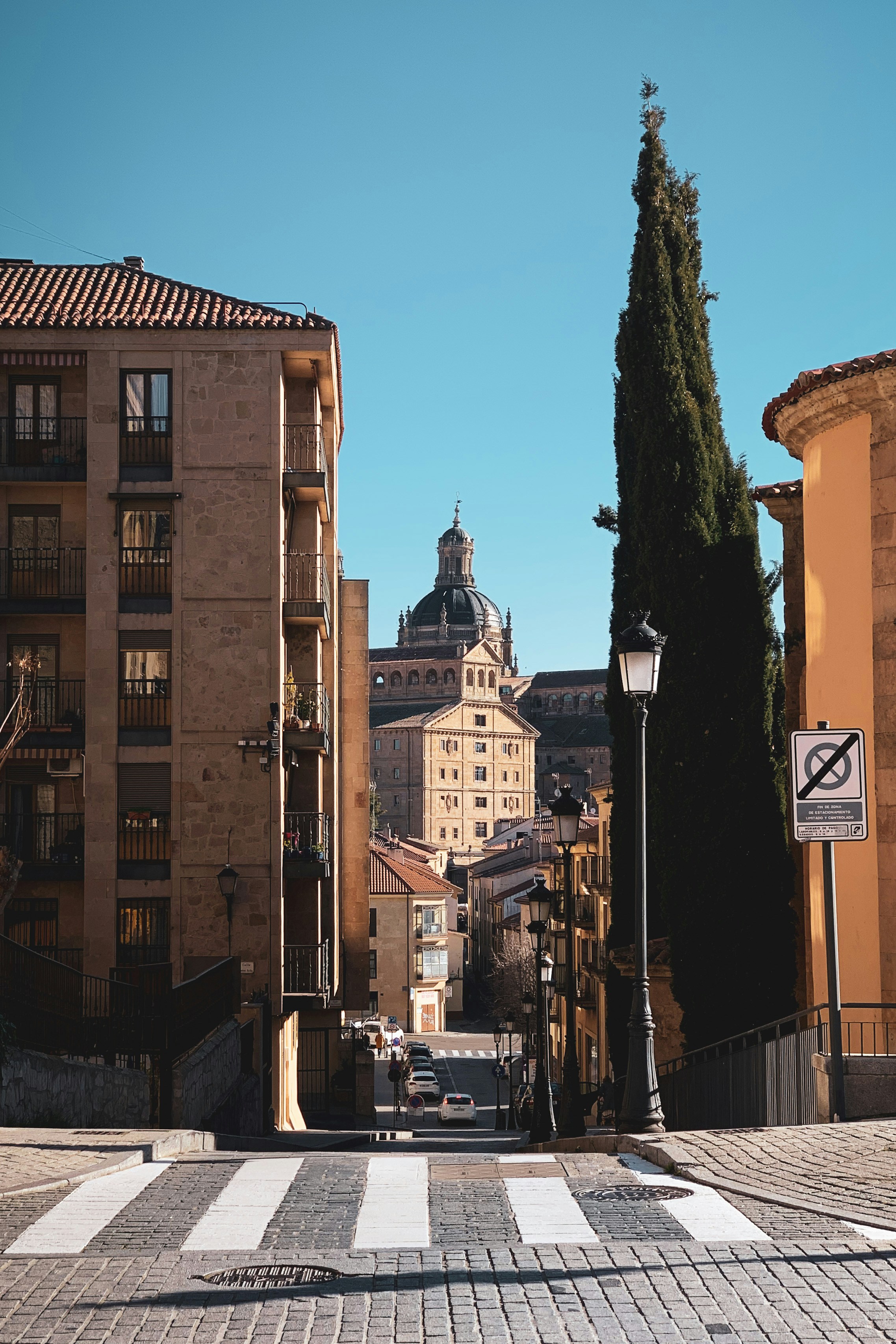 Narrow street flanked by historic buildings leading to a distant cathedral under a clear blue sky.