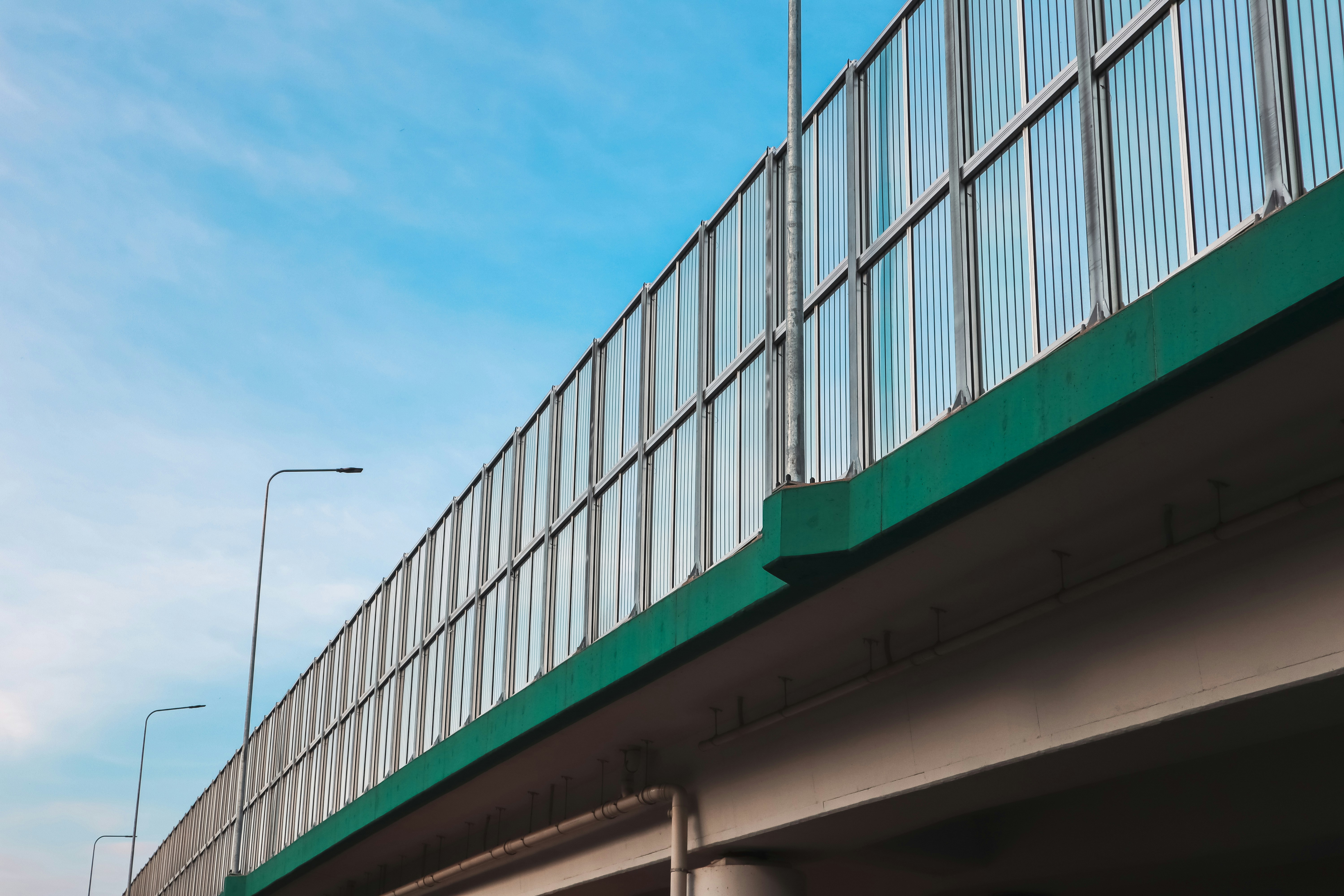 Concrete overpass with green accents and metal railings under a clear blue sky.