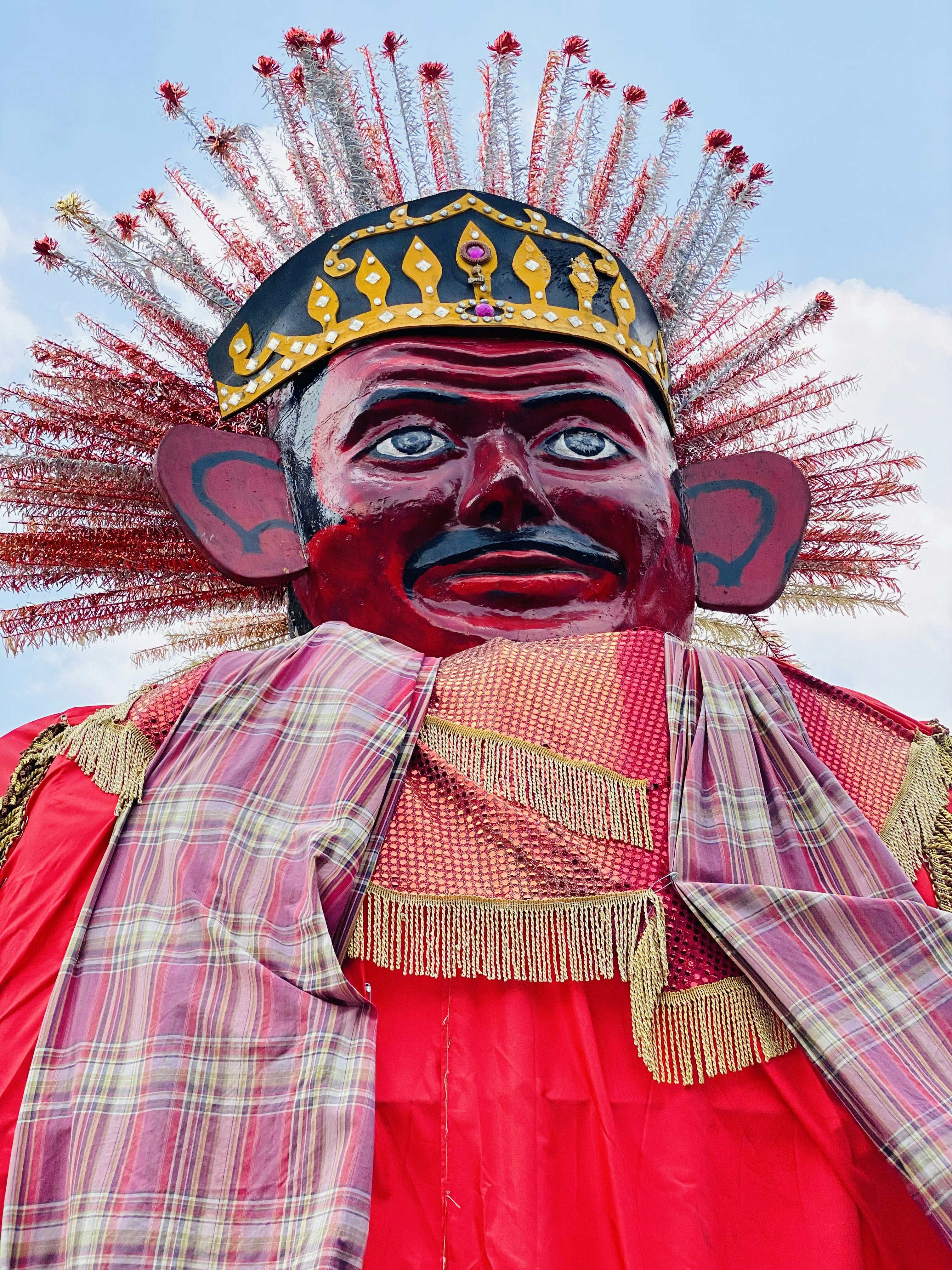 A large, colorful effigy adorned with intricate decorations and a striking headdress, representing cultural heritage. The vibrant red and gold elements highlight its significance.