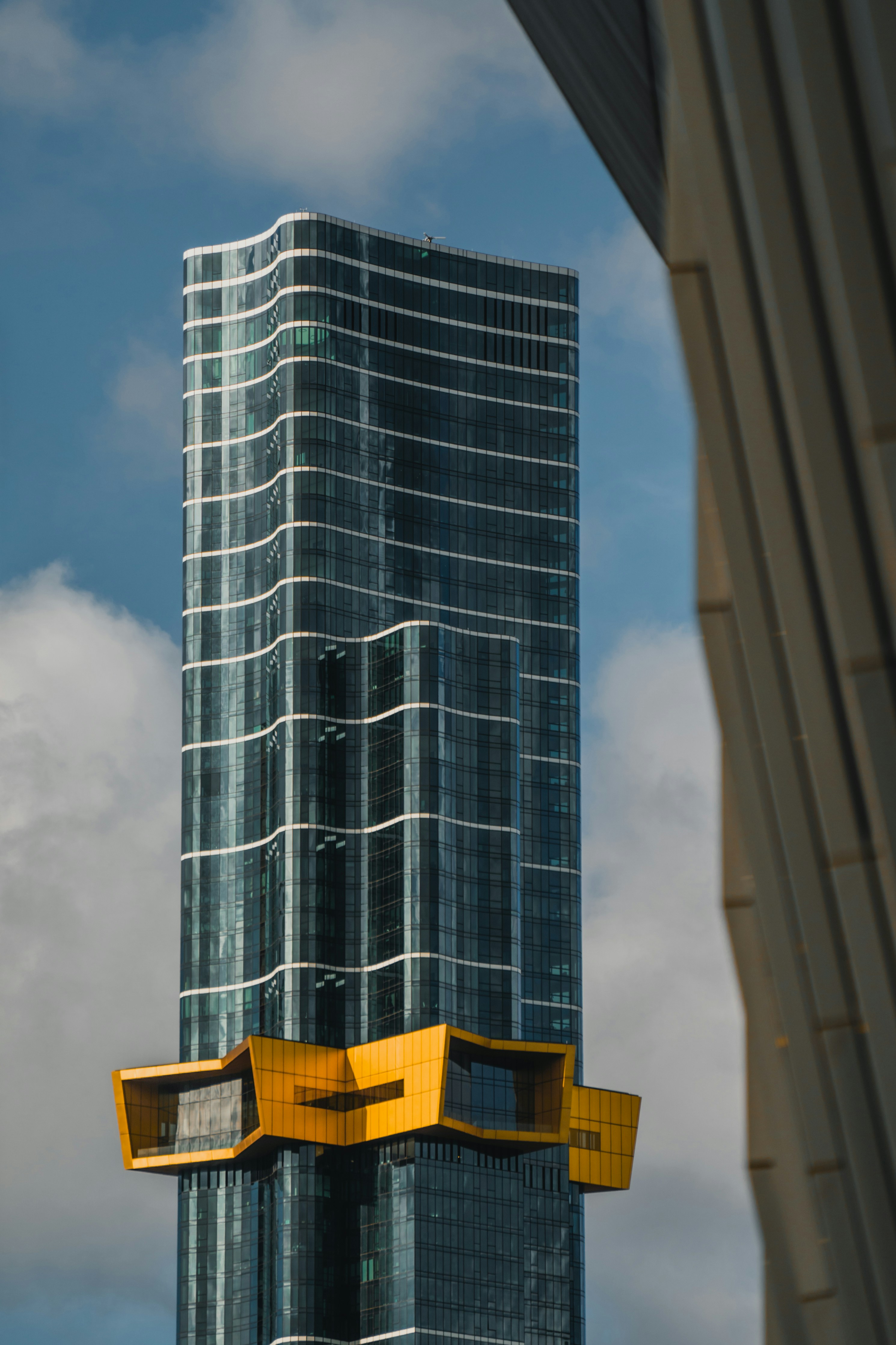 Yellow Bracketed Skyward: A Modern Tower With Wavy White Ribbon Facade