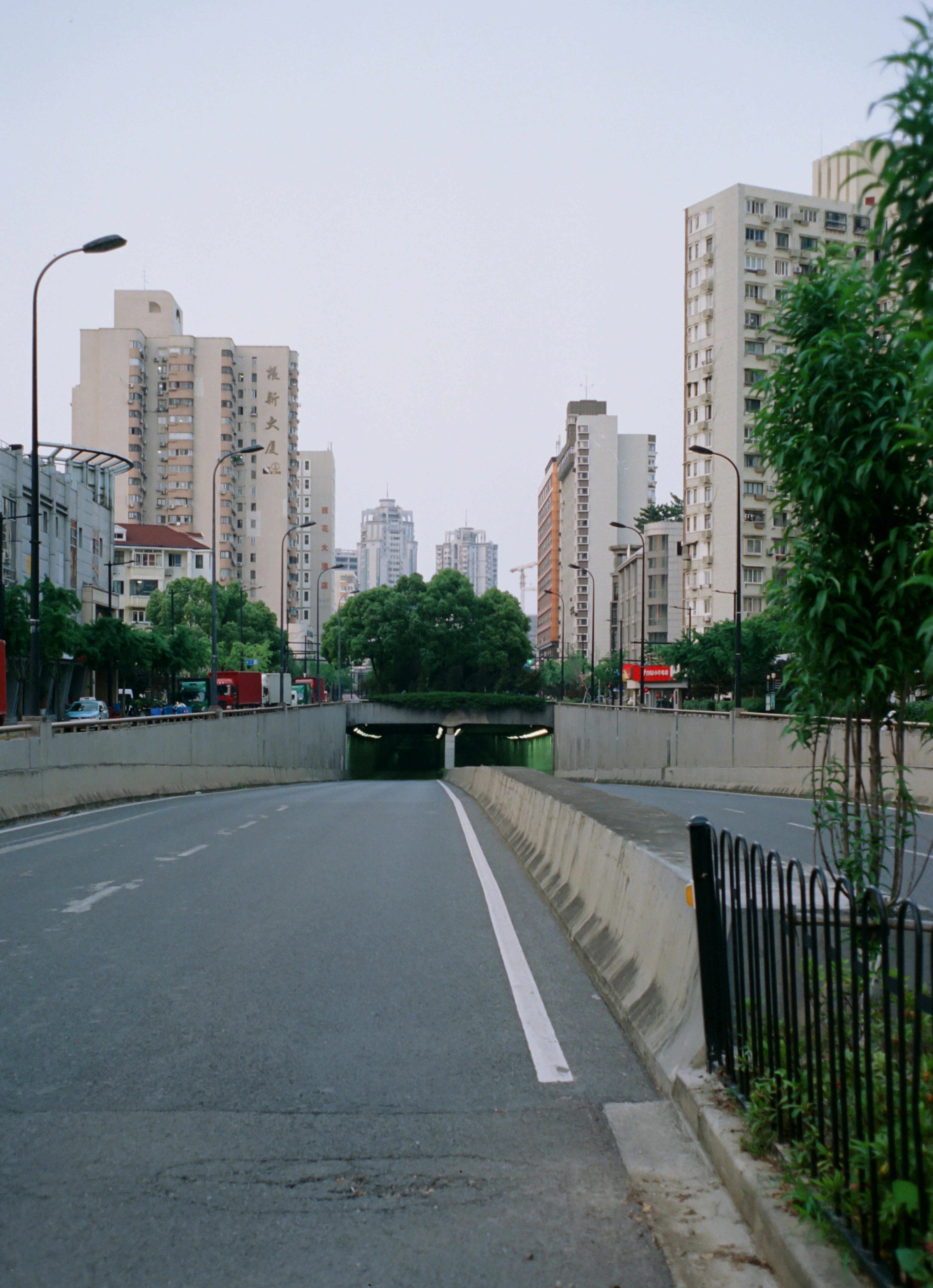 A wide road leading to an underground tunnel flanked by modern buildings and lush greenery, showcasing urban architecture and infrastructure.