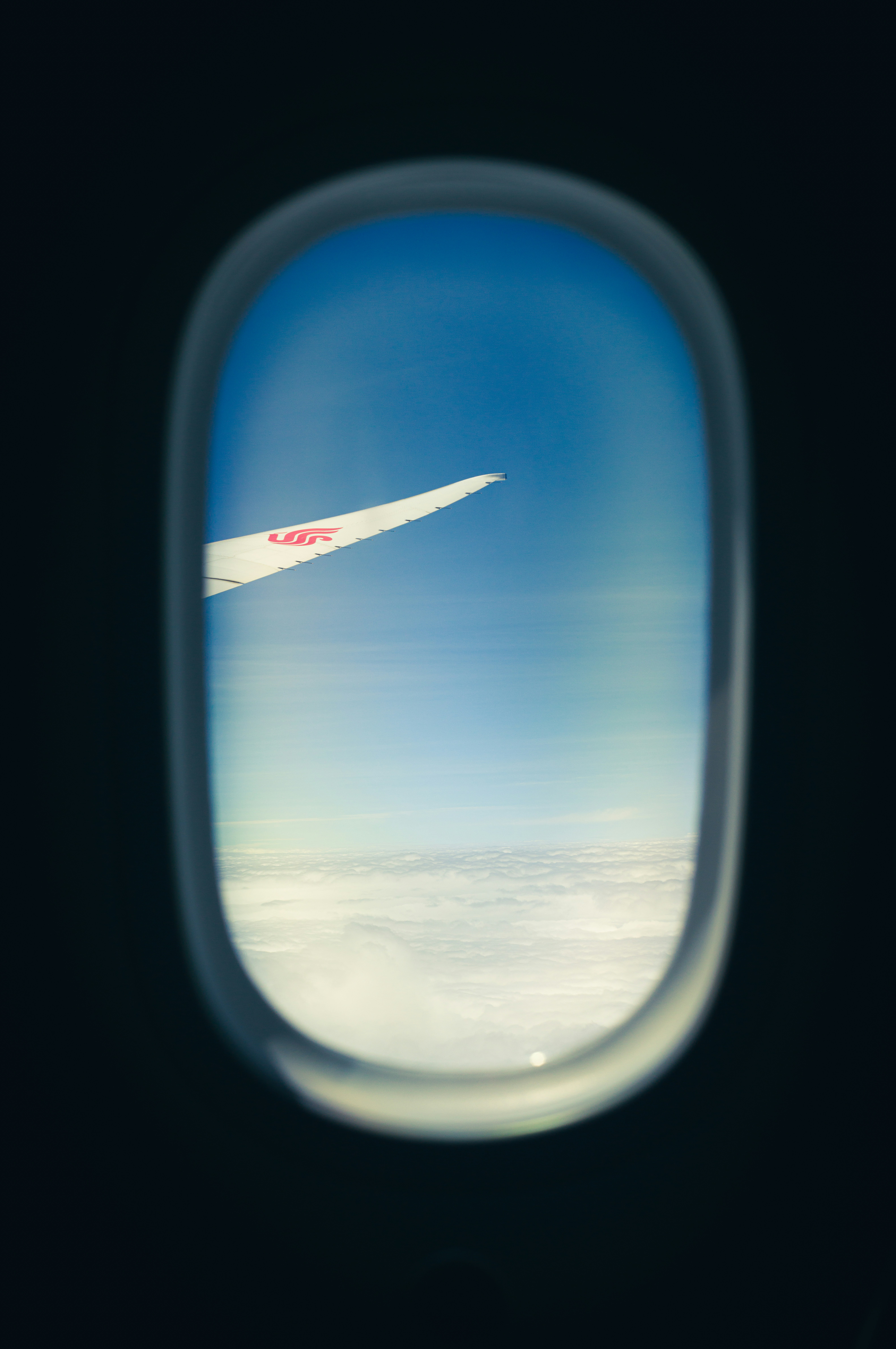 Photo from an airplane window showing a wingtip against a blue sky and a layer of clouds beneath.