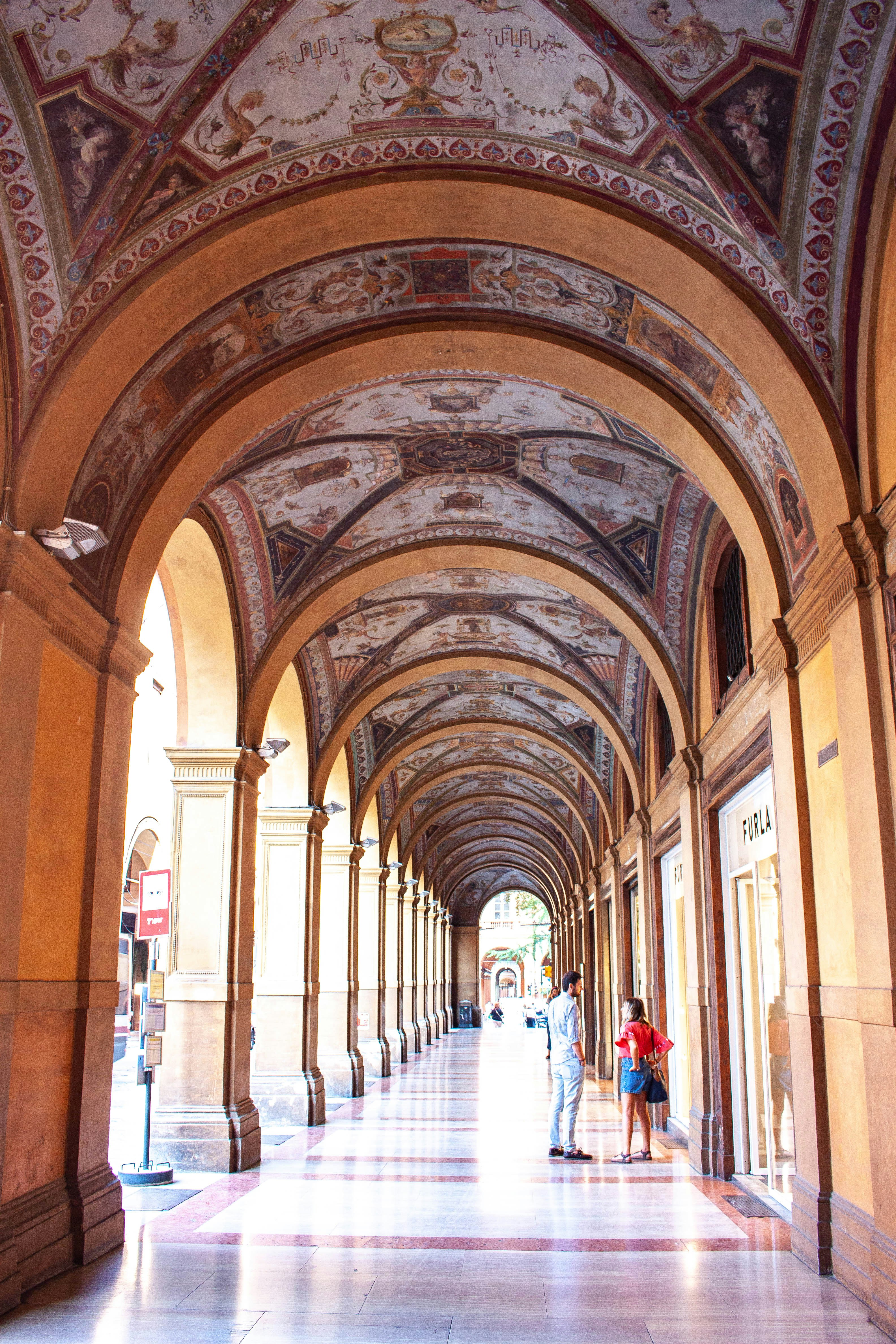 A couple of people walking through a building with arched ceilings ...