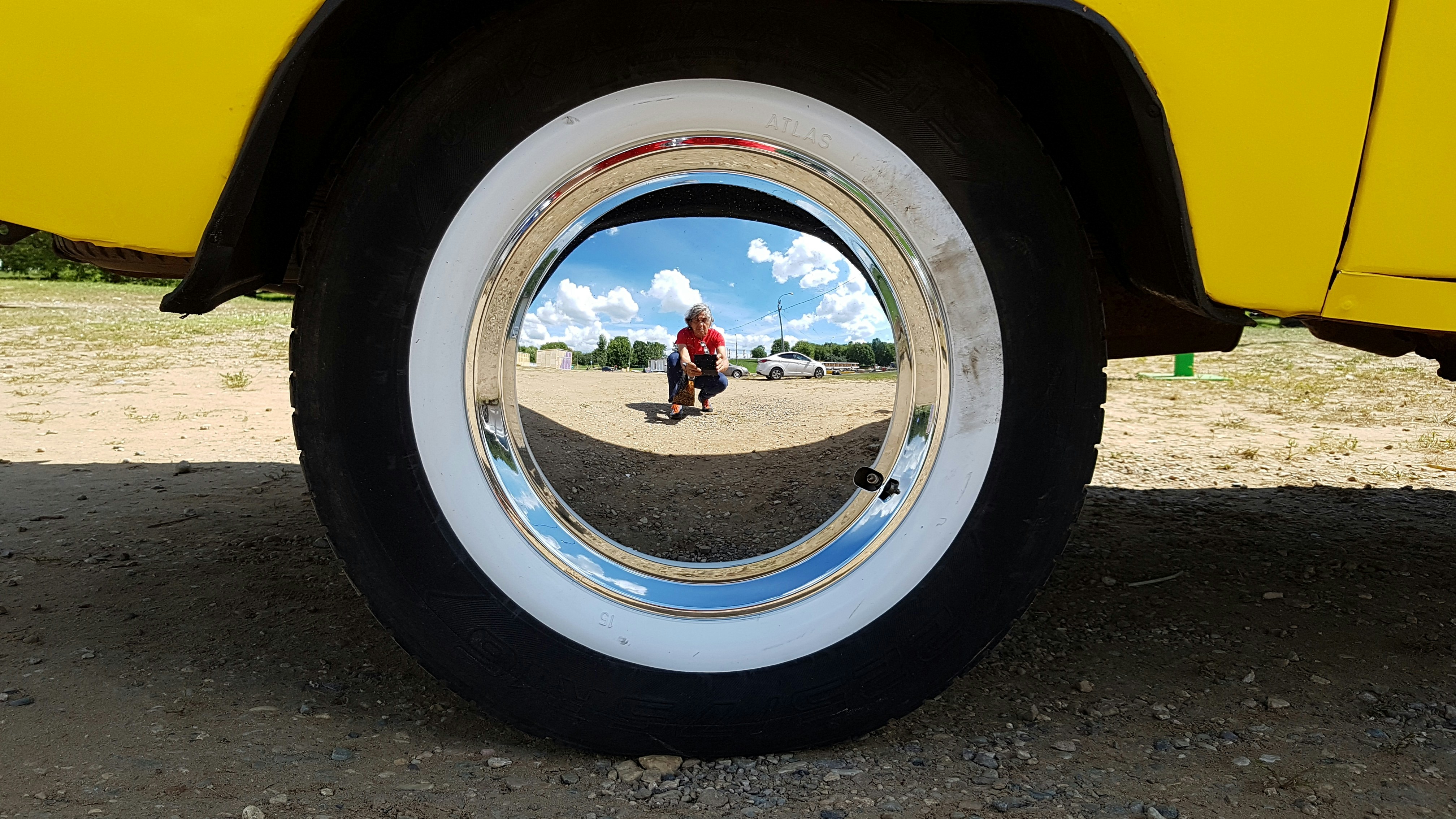 Chrome Ring Reflection: A Red-shirt Figure in the Wheel of a Yellow Vehicle