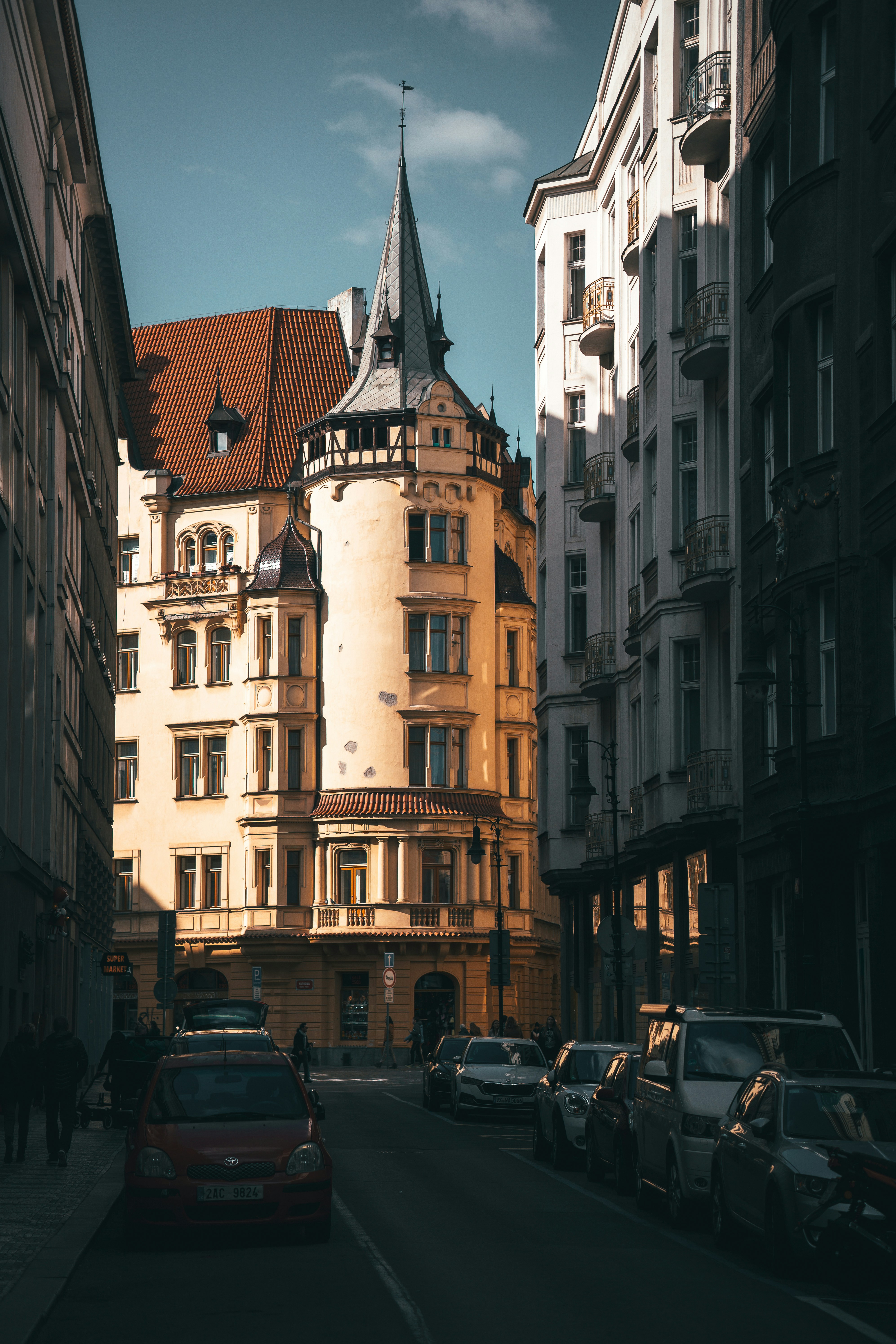Historic building with a distinctive turret and ornate details nestled between modern structures in a bustling city street.