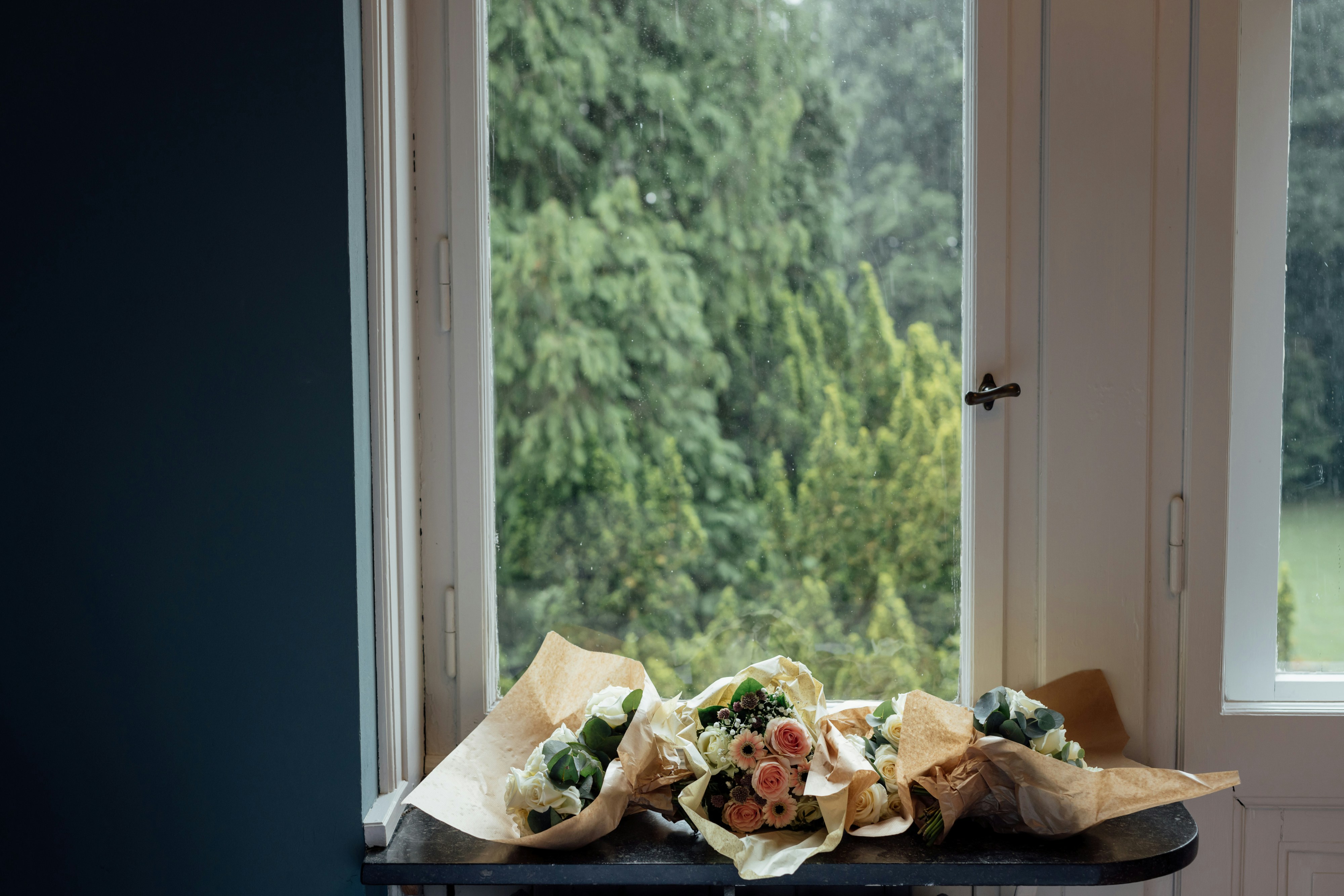 Bouquets of fresh flowers arranged on a table beside a large window overlooking lush greenery. The natural light enhances the vibrant colors of the blooms.