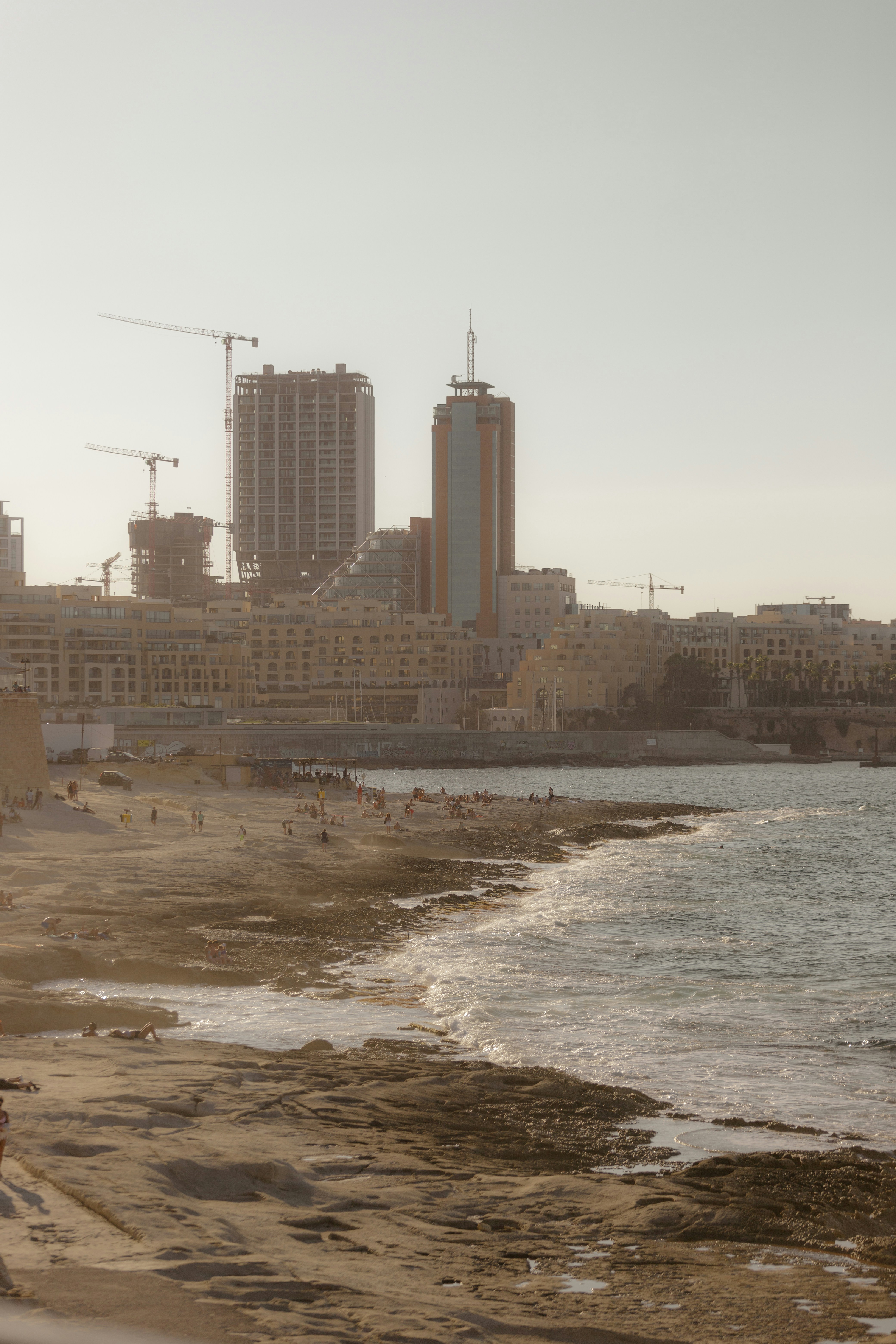 Urban shoreline: construction cranes rise behind a sunlit beach