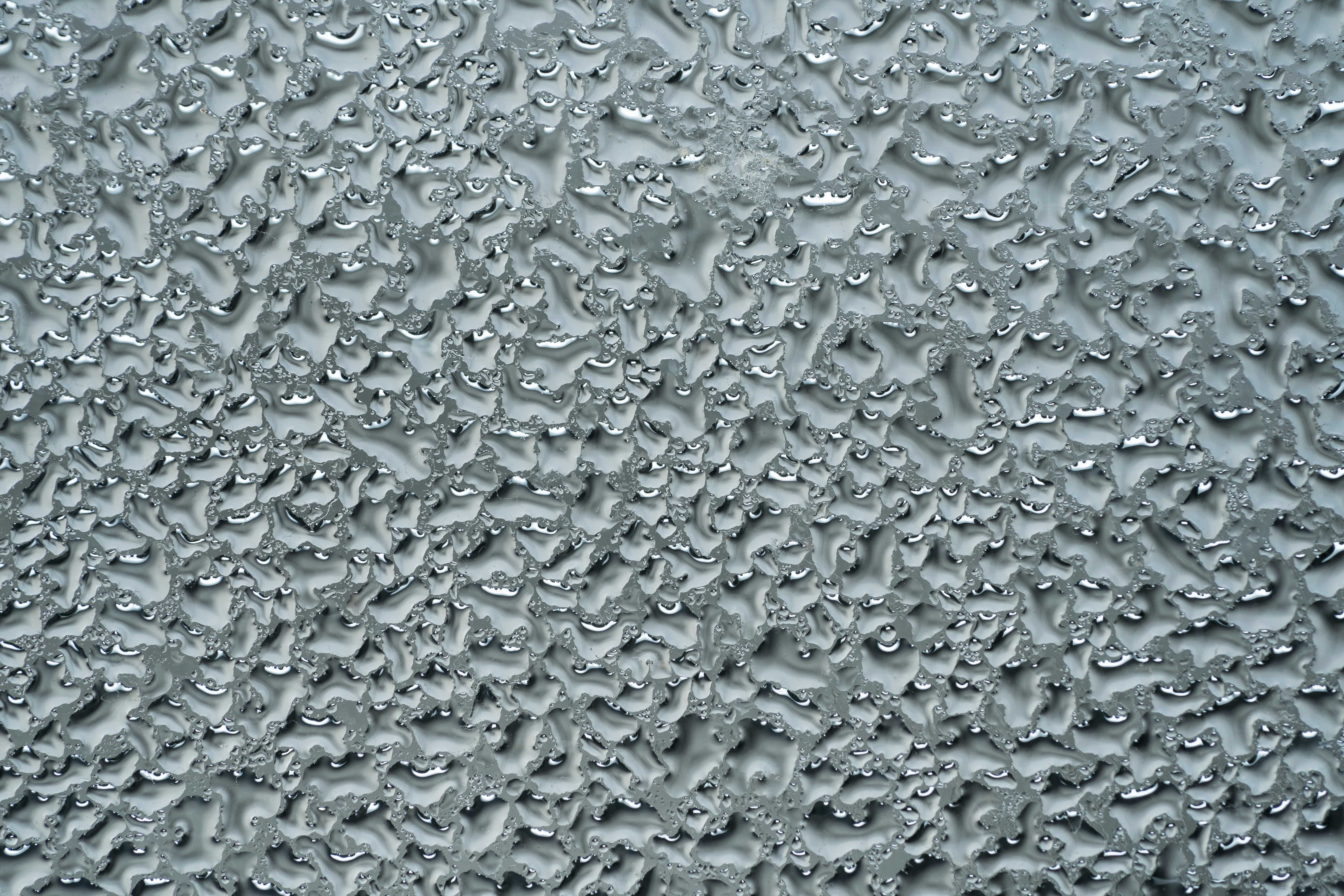 Close-up of numerous water droplets clinging to a textured surface, showcasing intricate patterns and reflections.