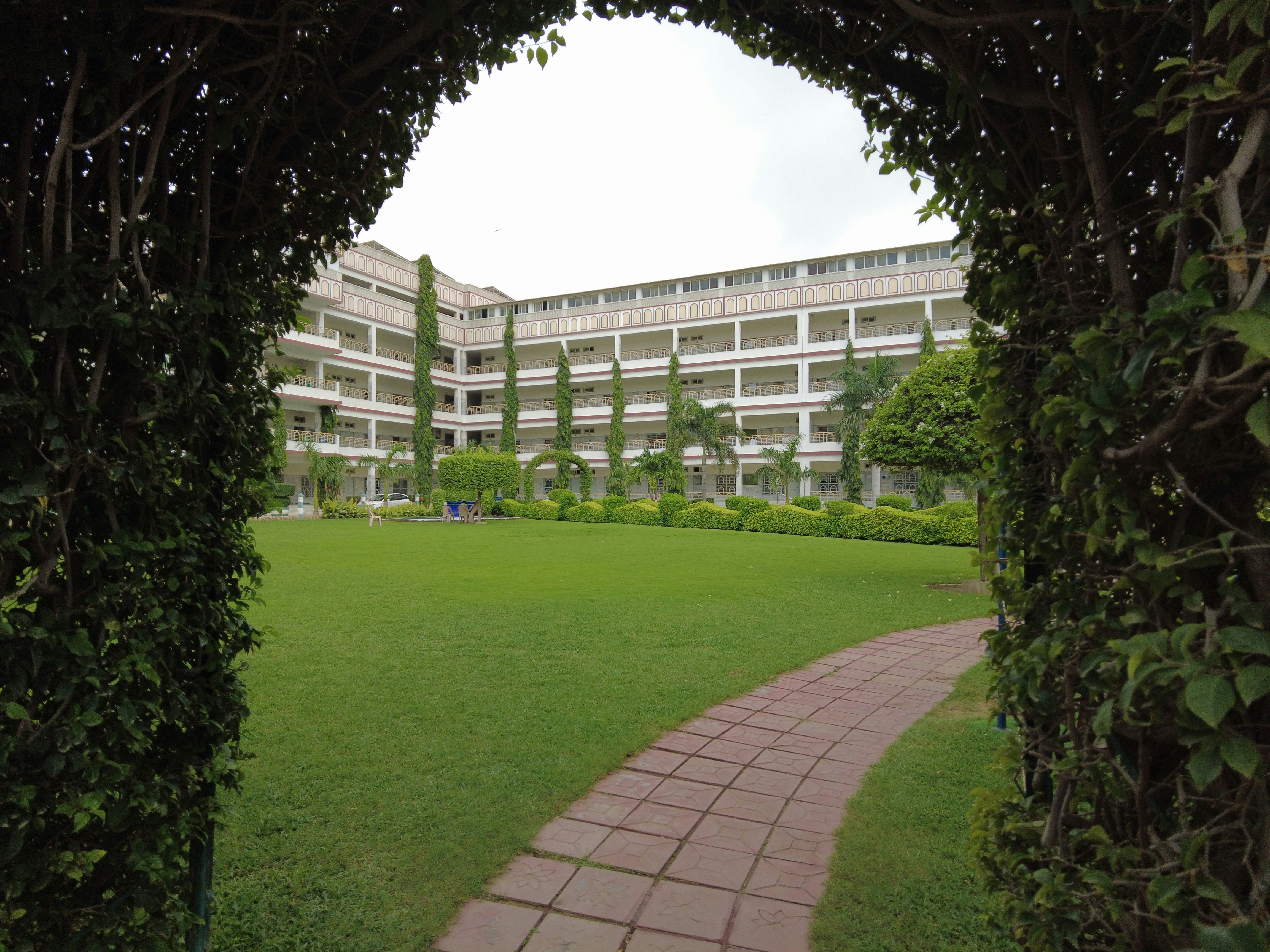 Lush green arch frames a campus courtyard with a well-maintained lawn and towering building in the background.