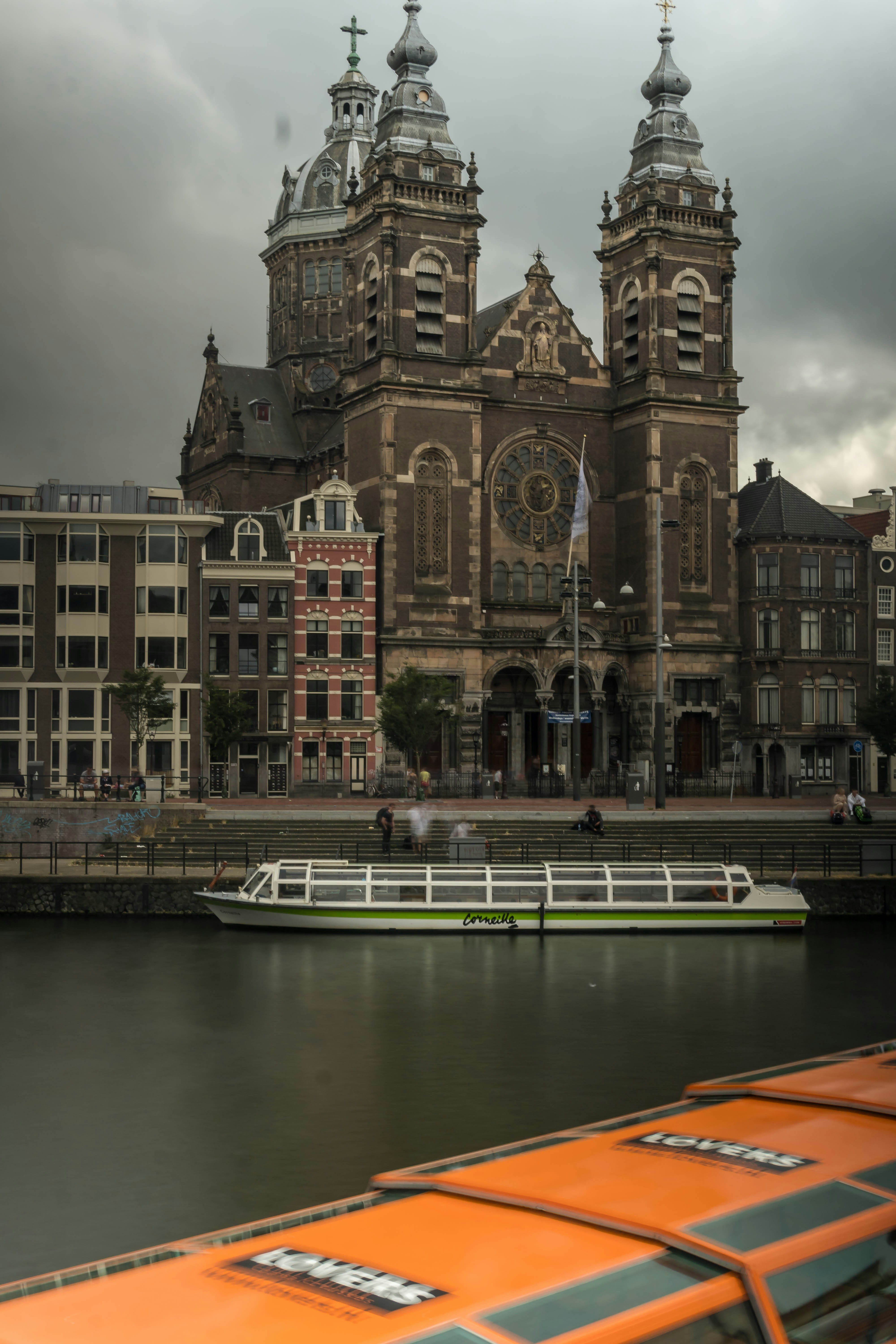 Historic church stands majestically along the waterfront, with a boat gliding past and modern buildings in the background.