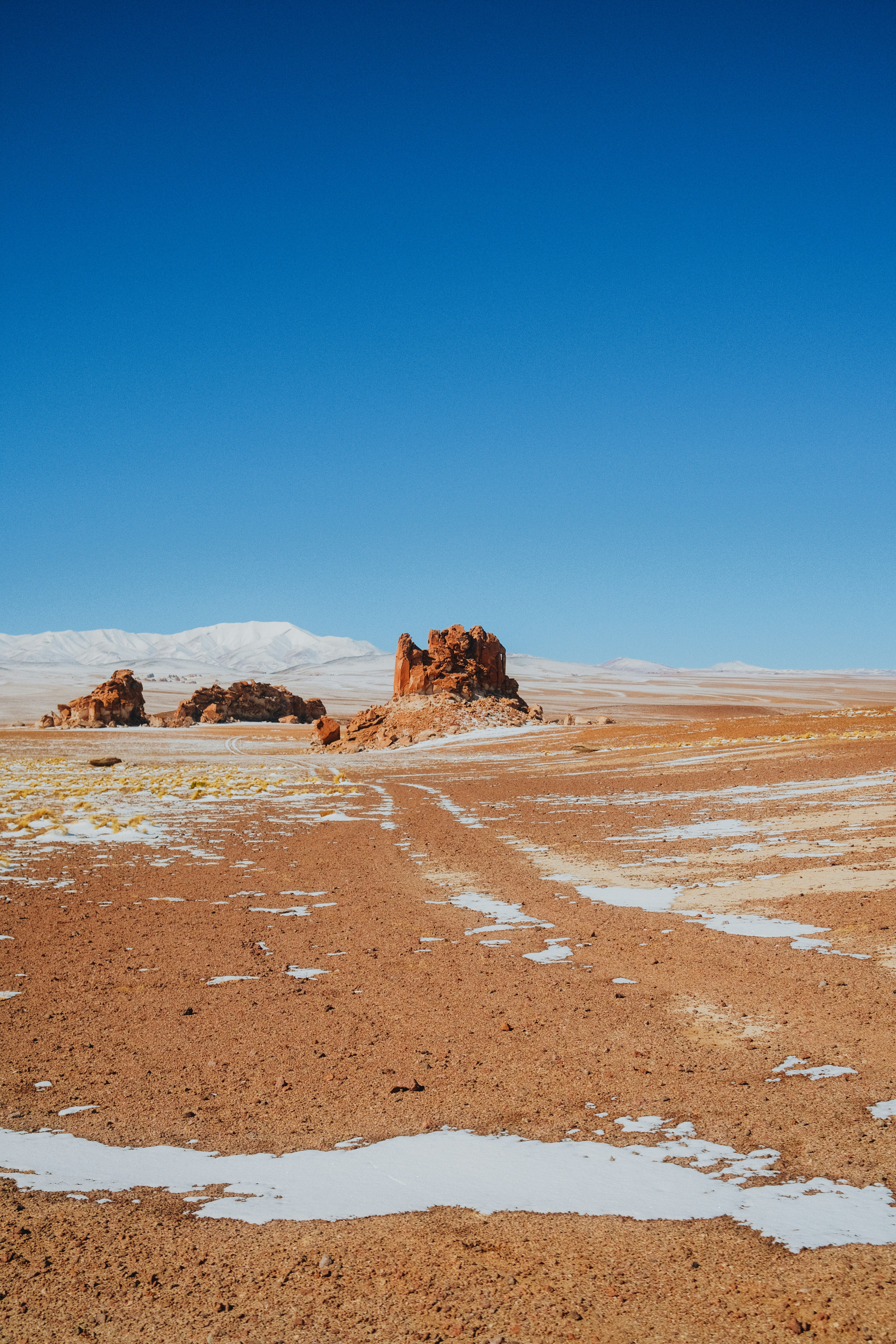View of landscape with a snowy desert and large rocky mountain formations and a subtle road path leading off into the distance.