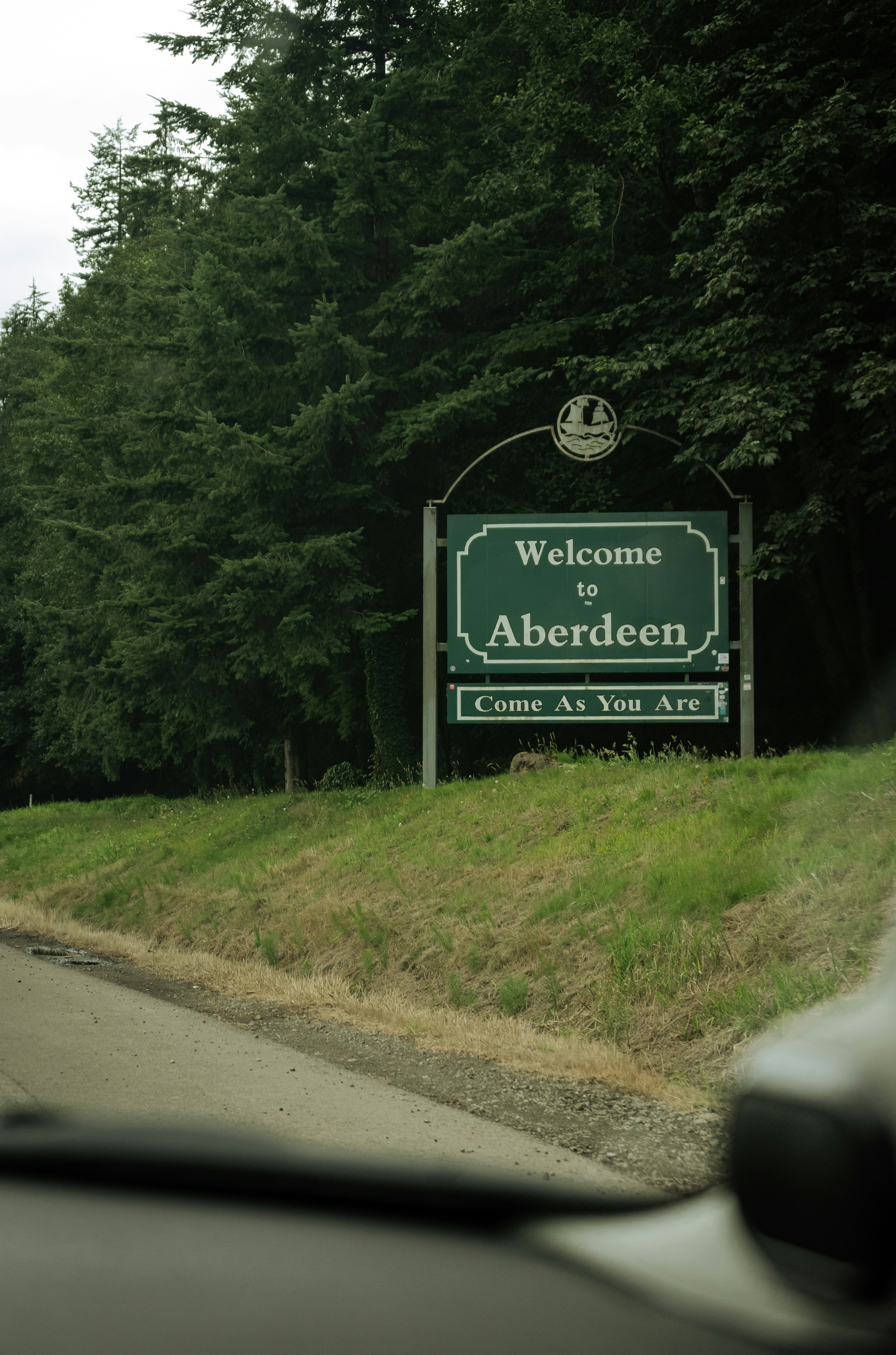 Welcome sign to Aberdeen flanked by lush trees under an overcast sky.