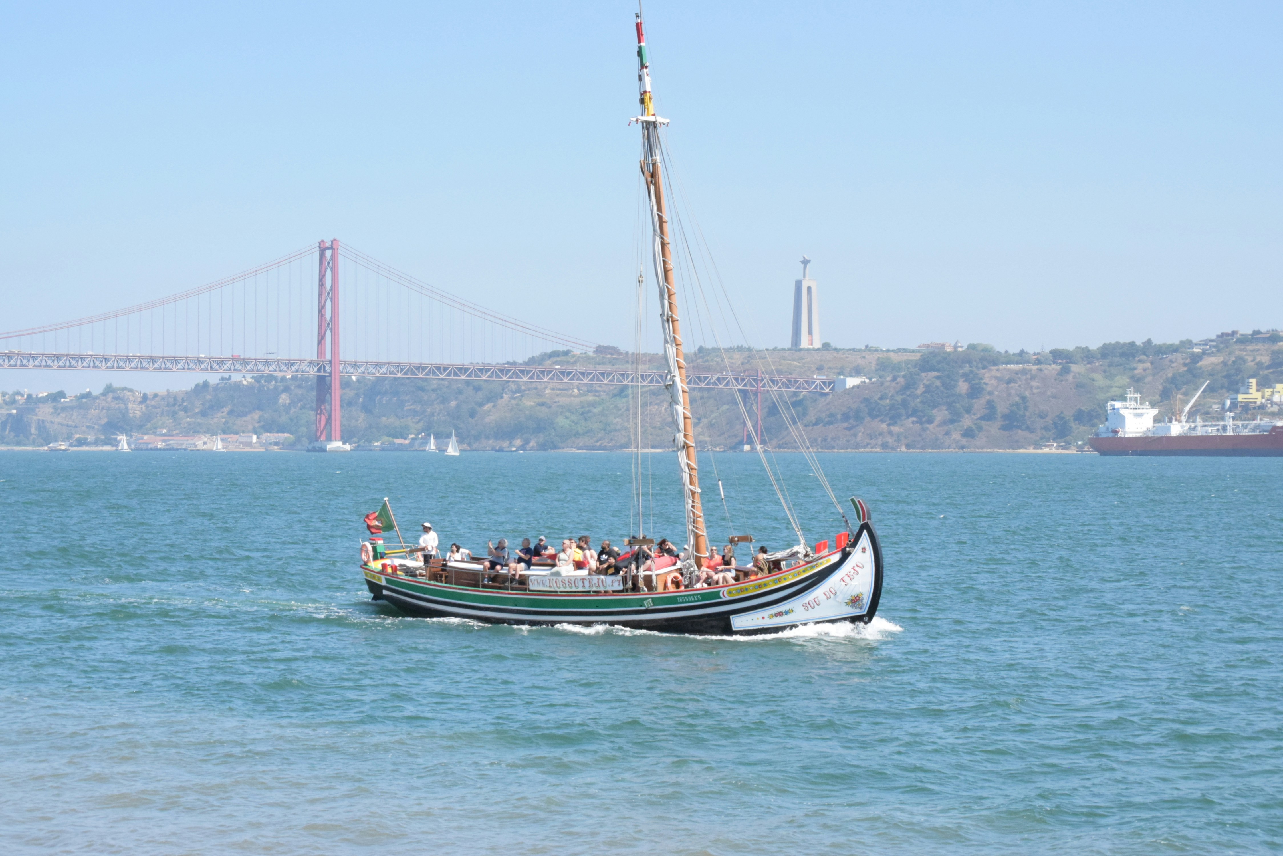 Lisbon Horizon: Crowded Traditional Sailboat Across Calm Atlantic Under a Red Bridge