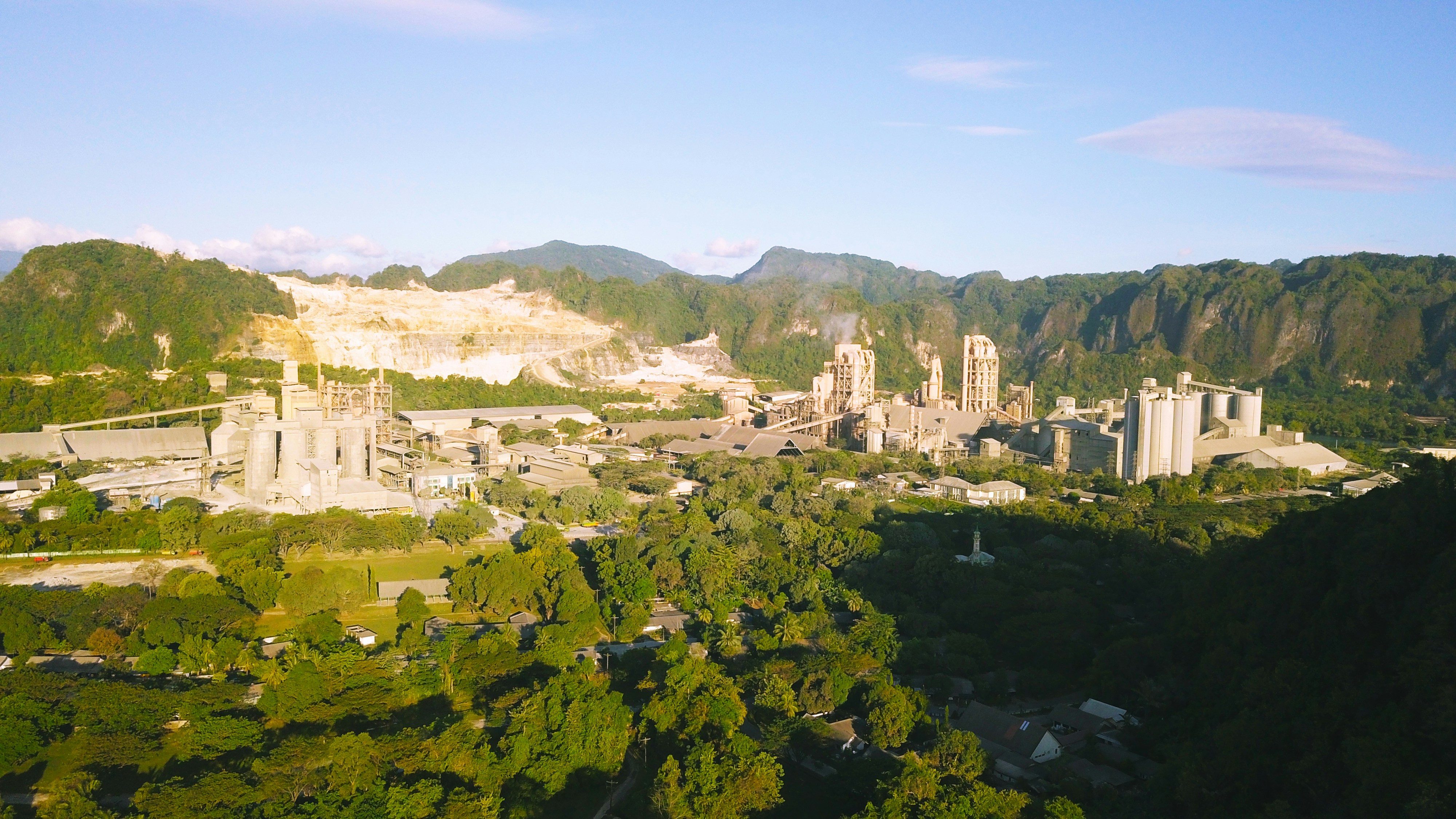 Cement factory nestled in lush hills under a clear blue sky.
