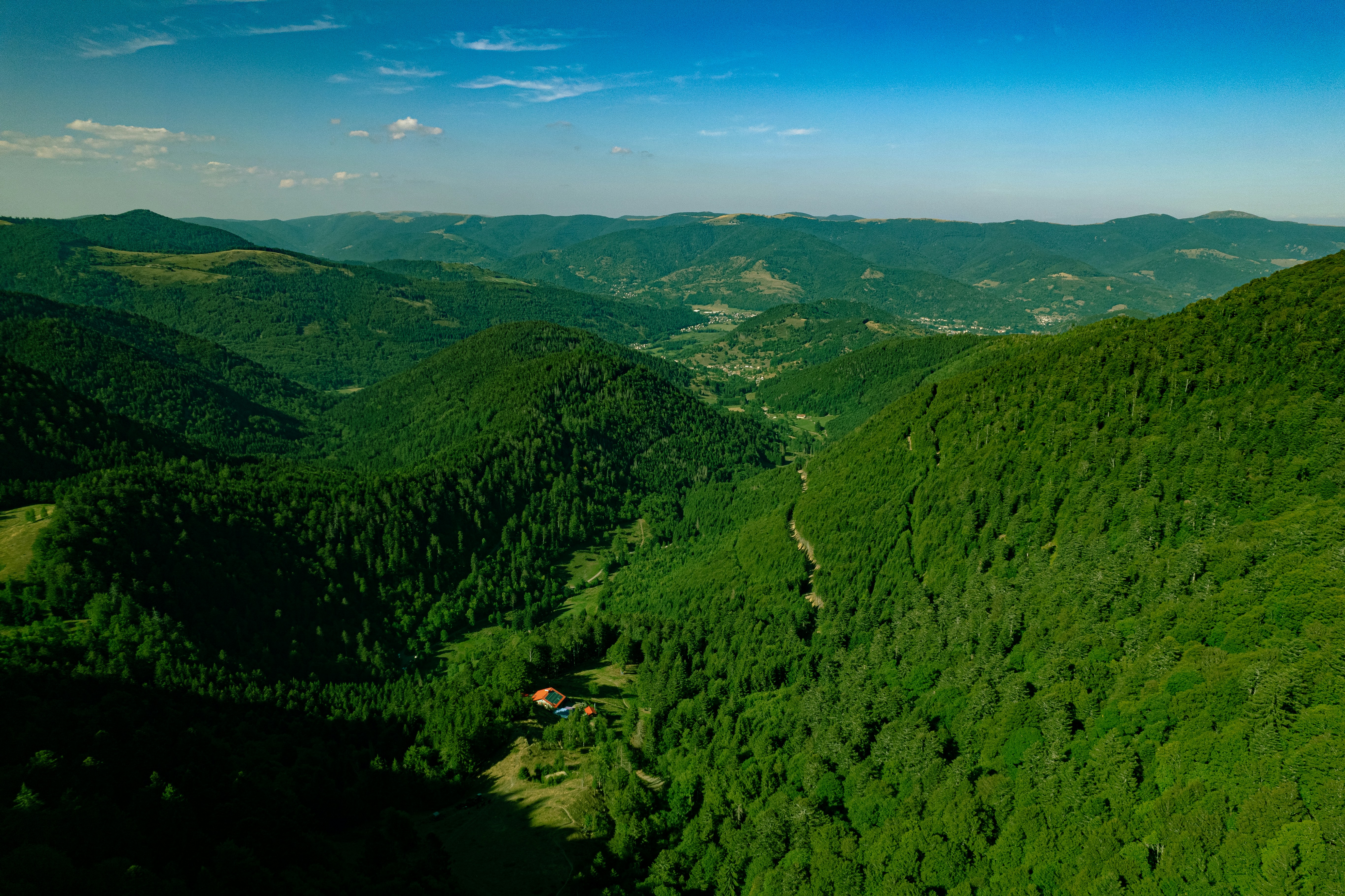 A secluded house nestles in a lush green valley surrounded by rolling hills under a clear blue sky.