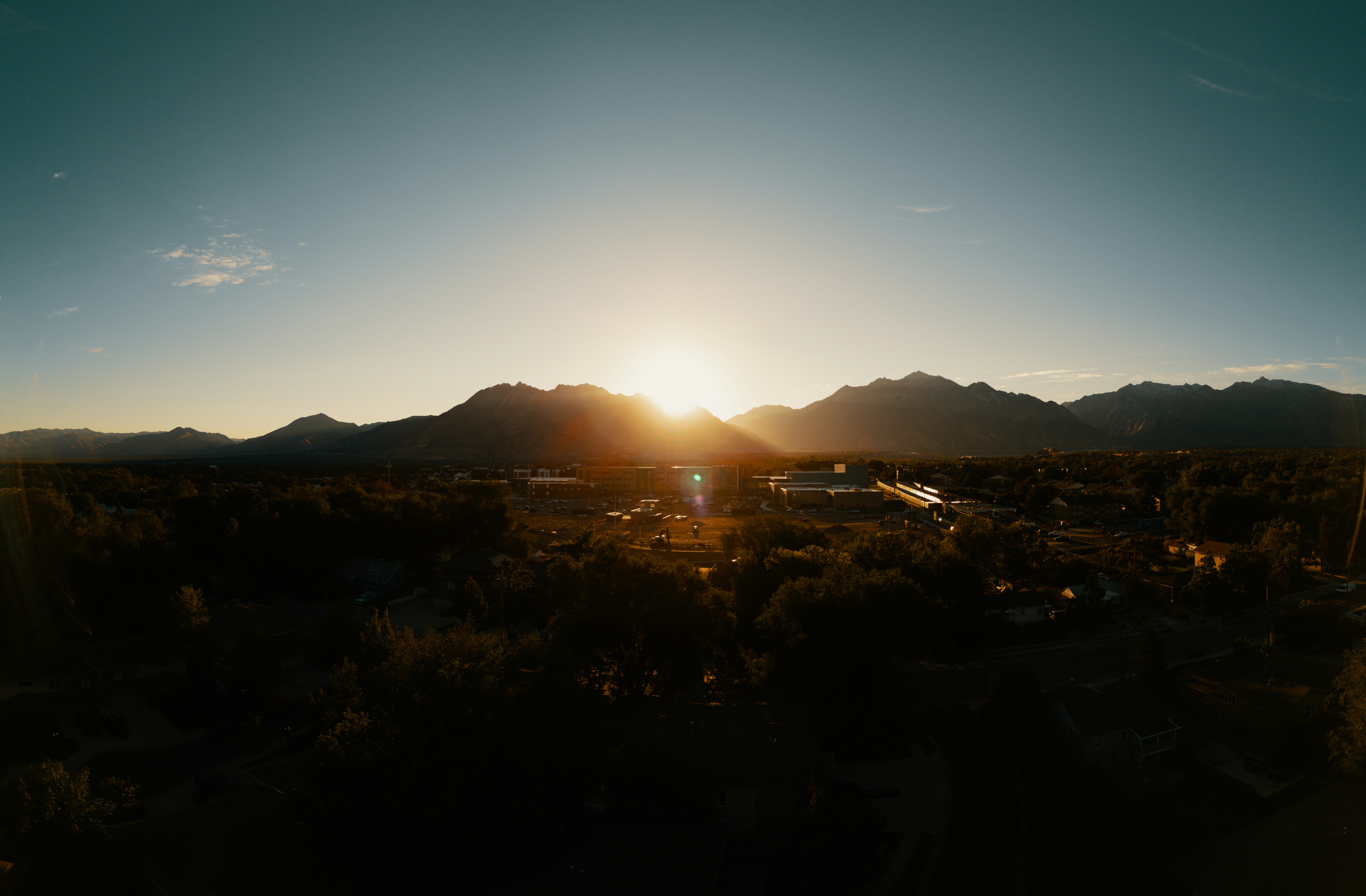 Sun peeking over mountain range, casting light across a tranquil valley.