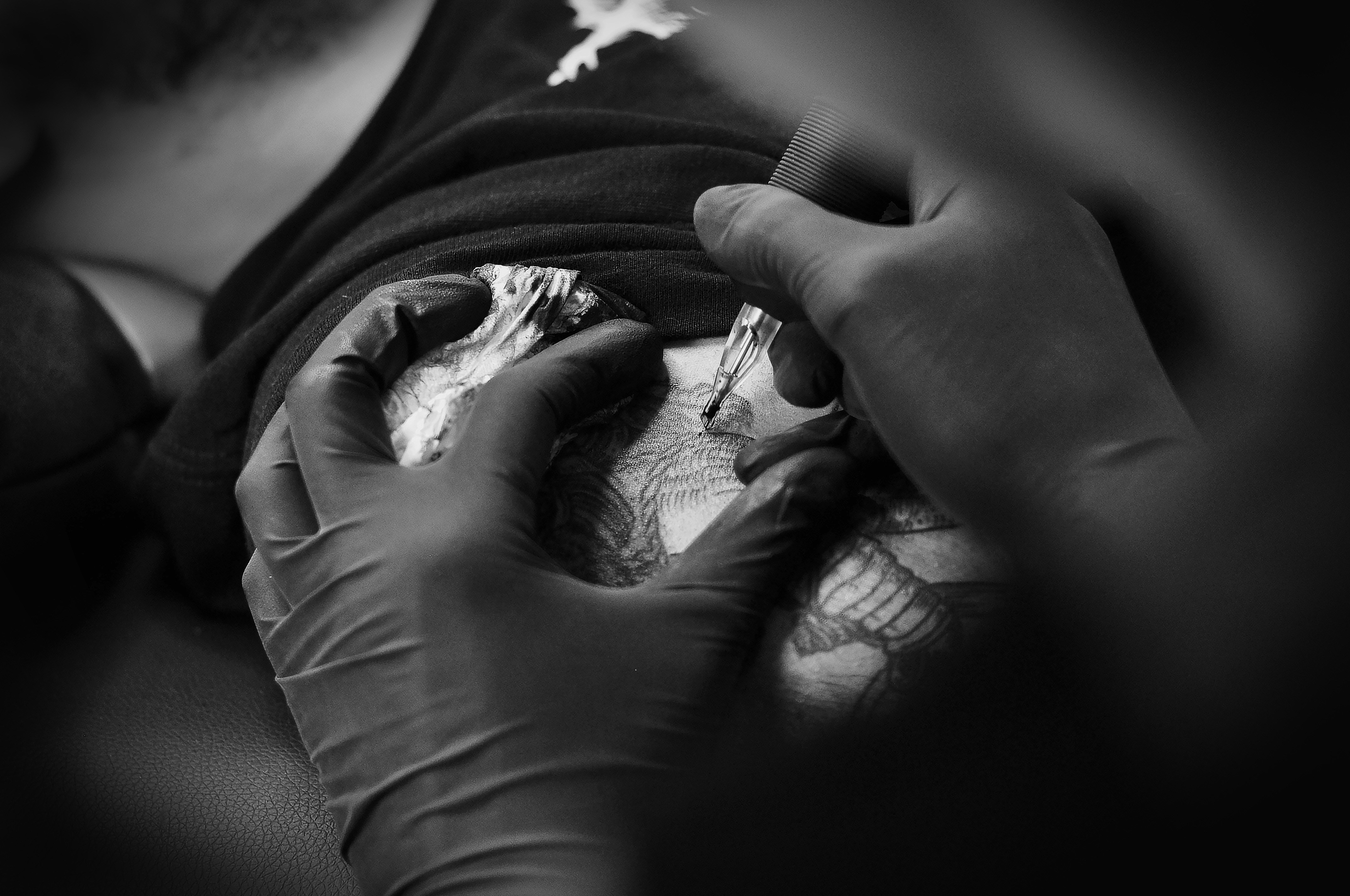 Tattoo artist's hands working intricately on a client's skin, captured in monochrome.