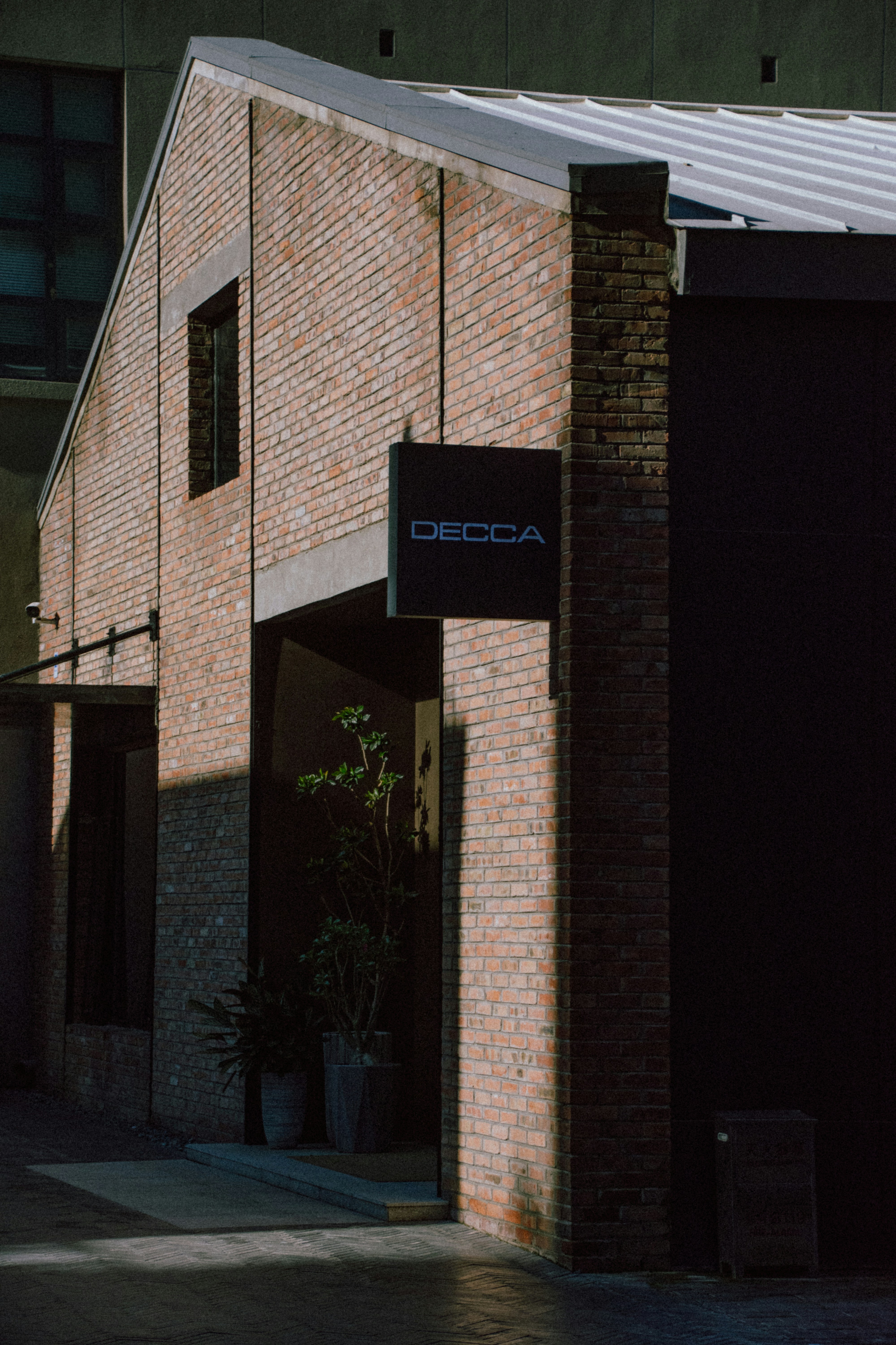 Stylish brick building featuring a prominent sign for DECCA, with subtle greenery enhancing the entrance.
