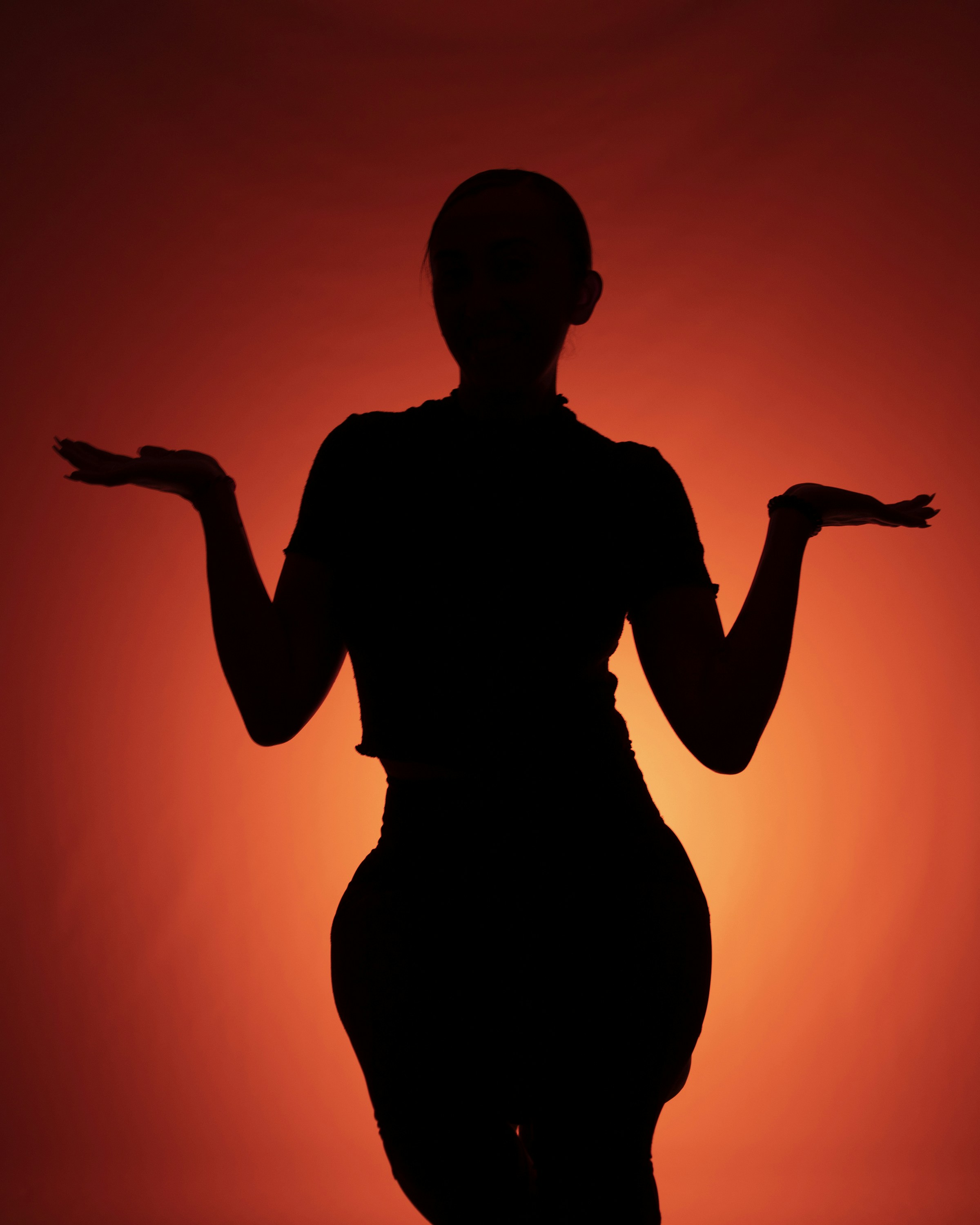 Silhouette of a figure gesturing with outstretched arms against a warm orange backdrop.