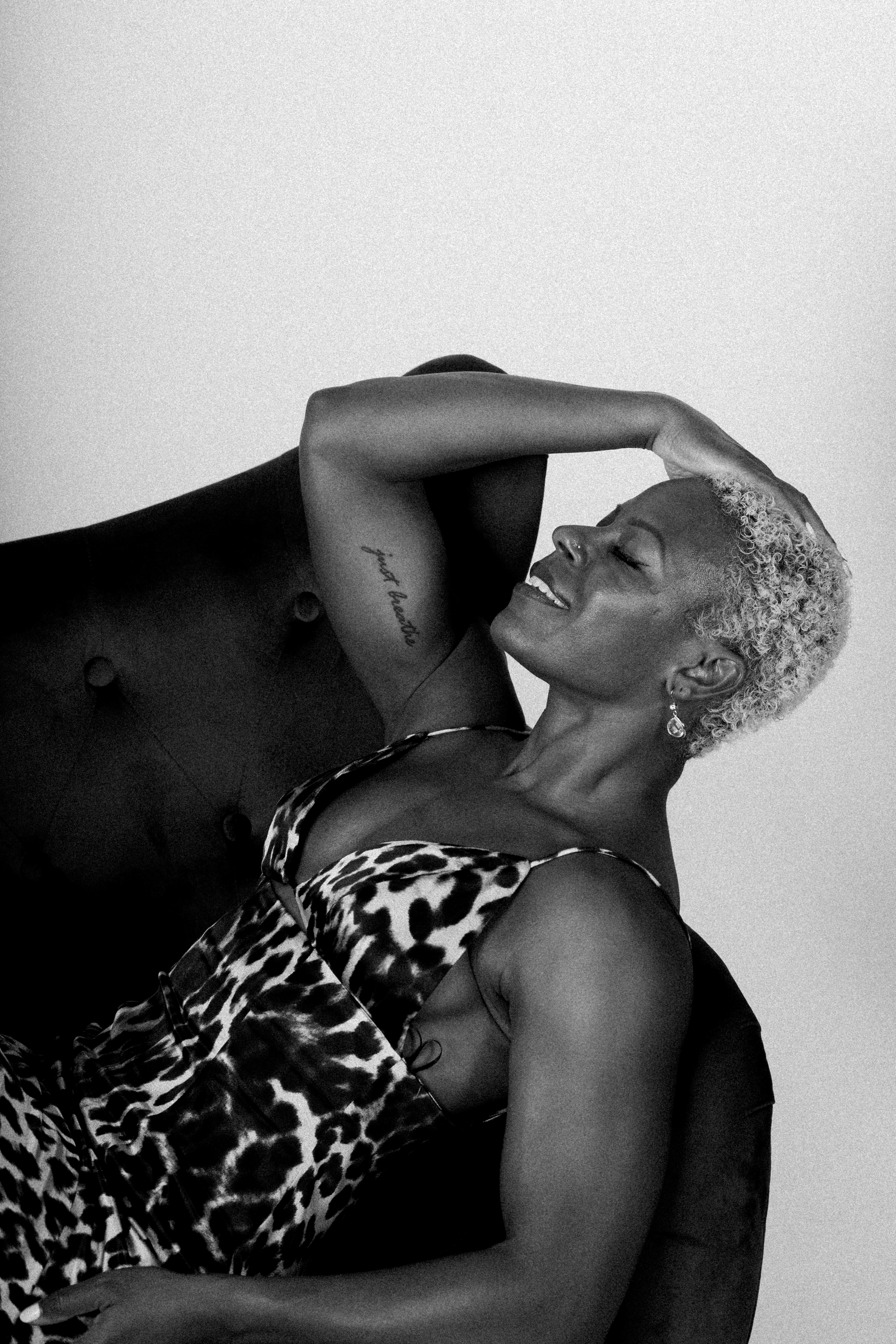 A woman reclines elegantly on a plush chair, showcasing her confidence and style with a striking leopard print dress and a serene expression.
