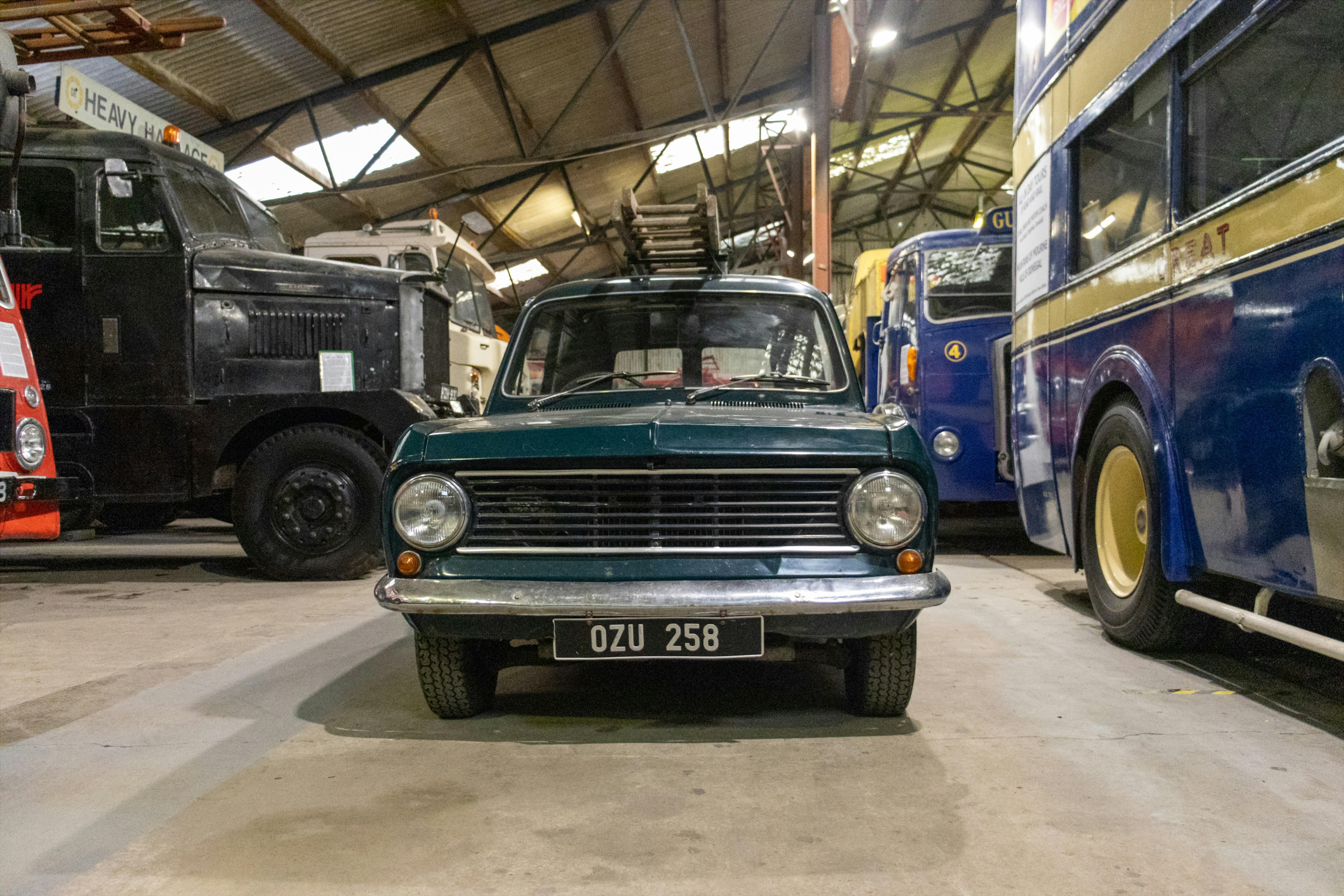 Center Stage: A Green Classic Sedan Guarding a Gallery of Vintage Buses