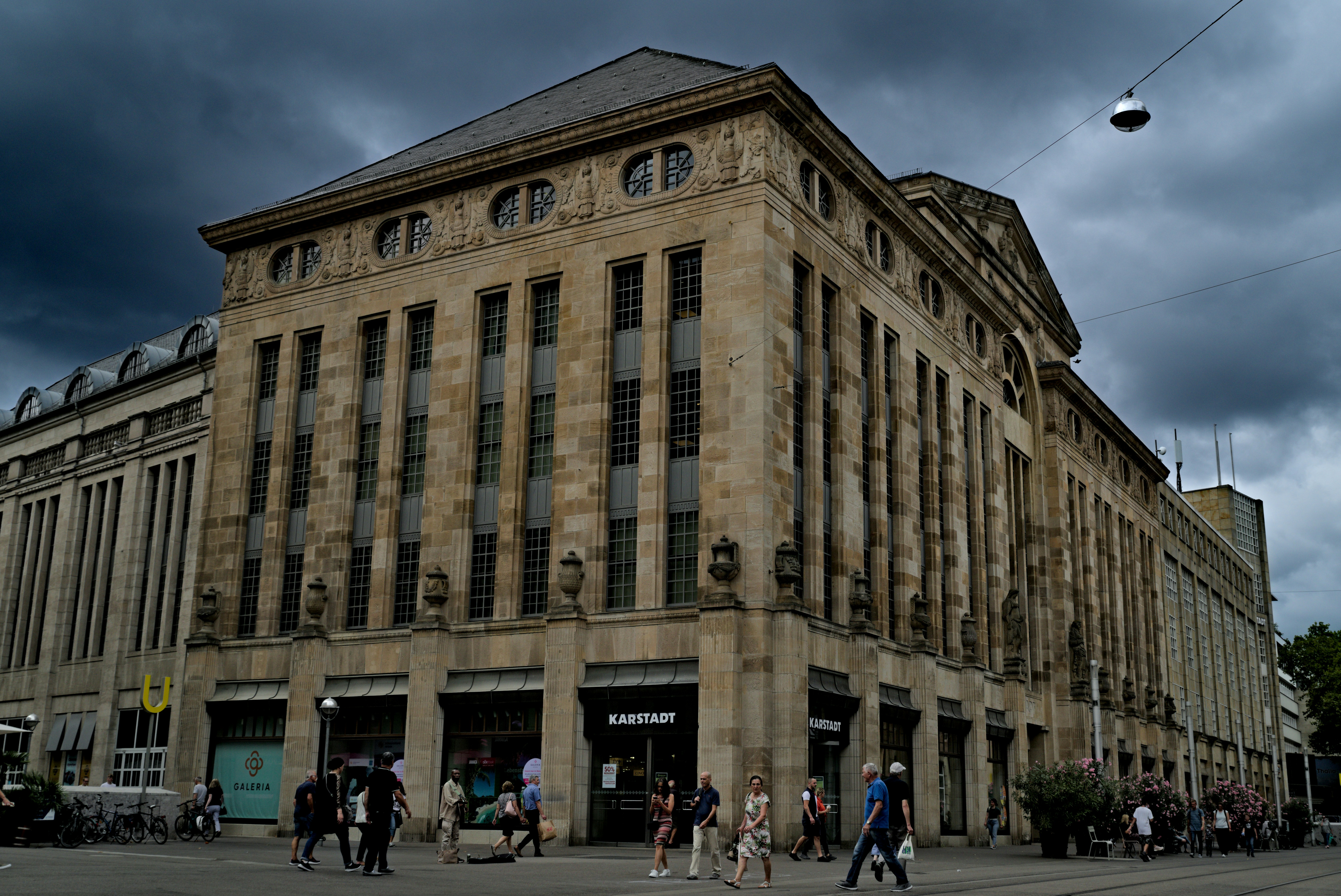 Historic building with a striking facade and large windows, bustling with pedestrians below a dramatic sky.